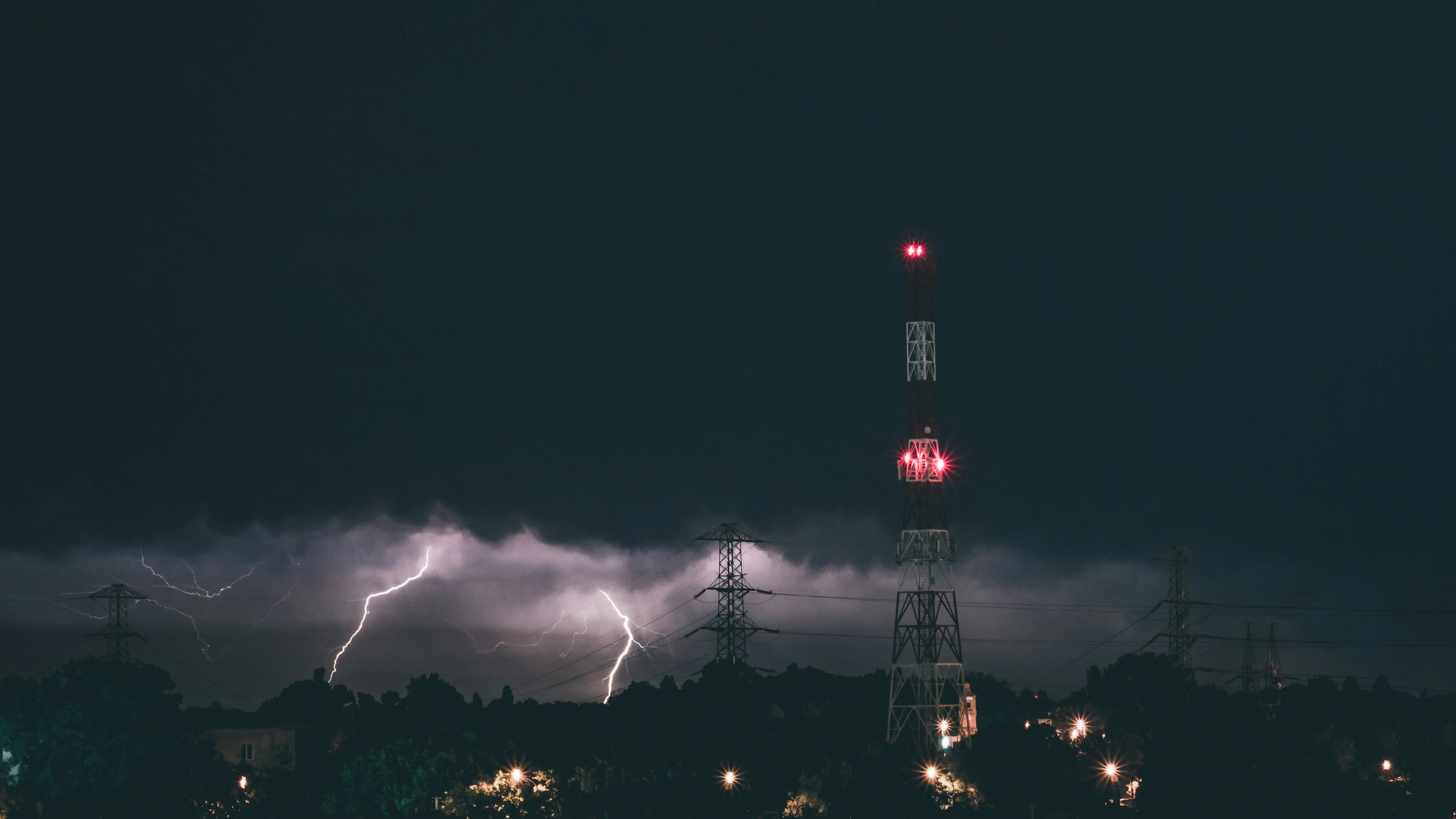Lightning strikes illuminate a dark sky near a communication tower, showcasing the raw power of nature against urban infrastructure.