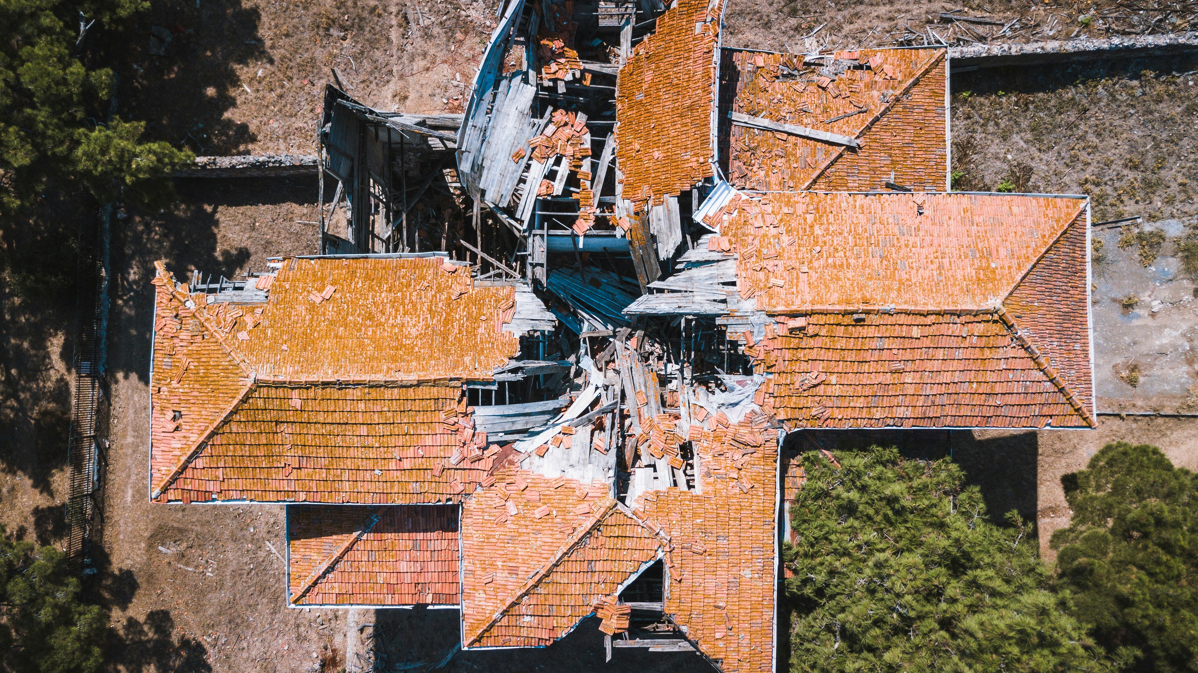 Aerial view of a dilapidated building with a collapsed roof, showcasing intricate tile patterns and surrounding overgrowth. The structure reflects a poignant history of neglect.
