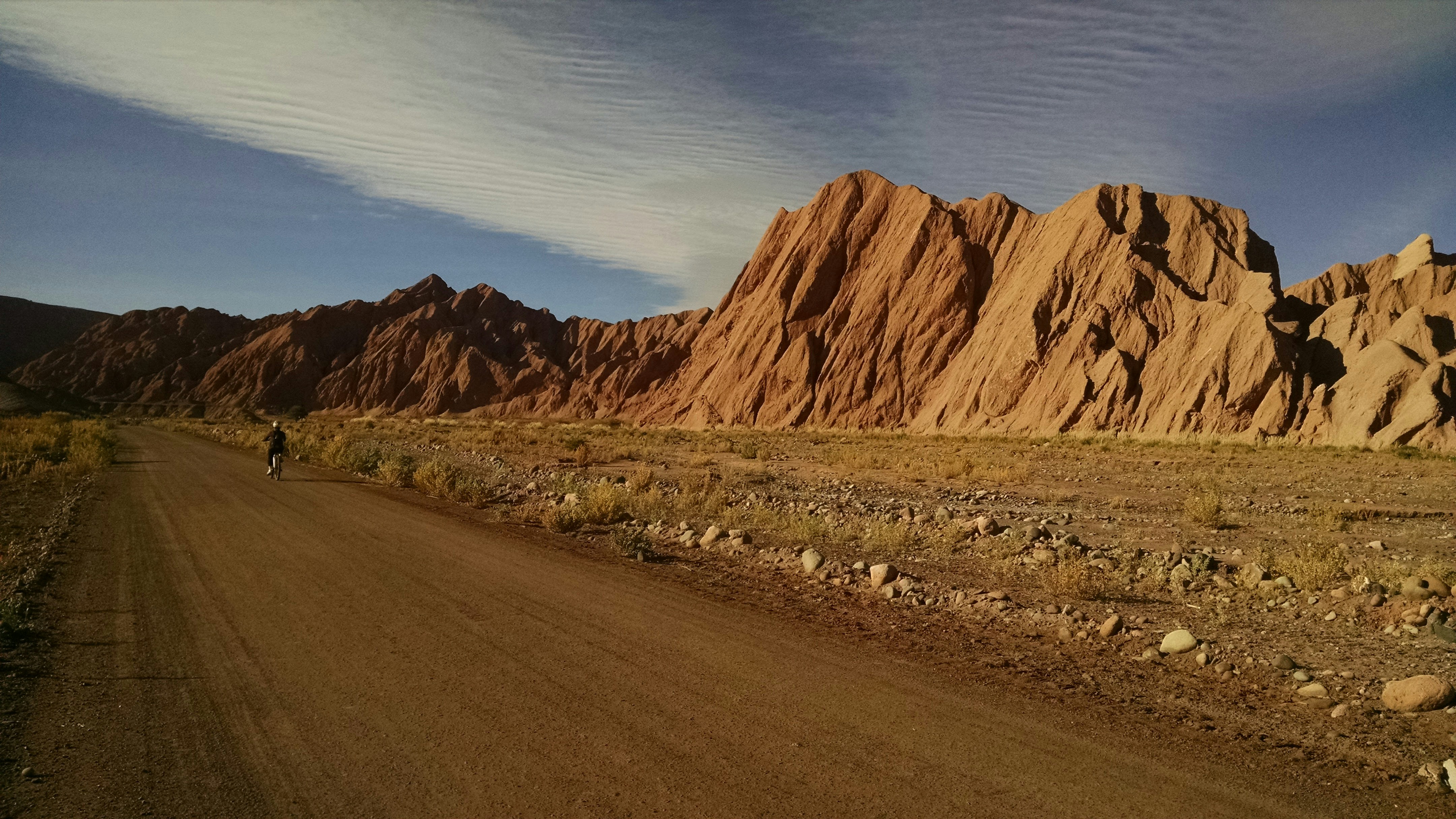 A lone cyclist traverses a rugged dirt road framed by striking rock formations under a vast sky. The scene captures the essence of adventure in a remote landscape.