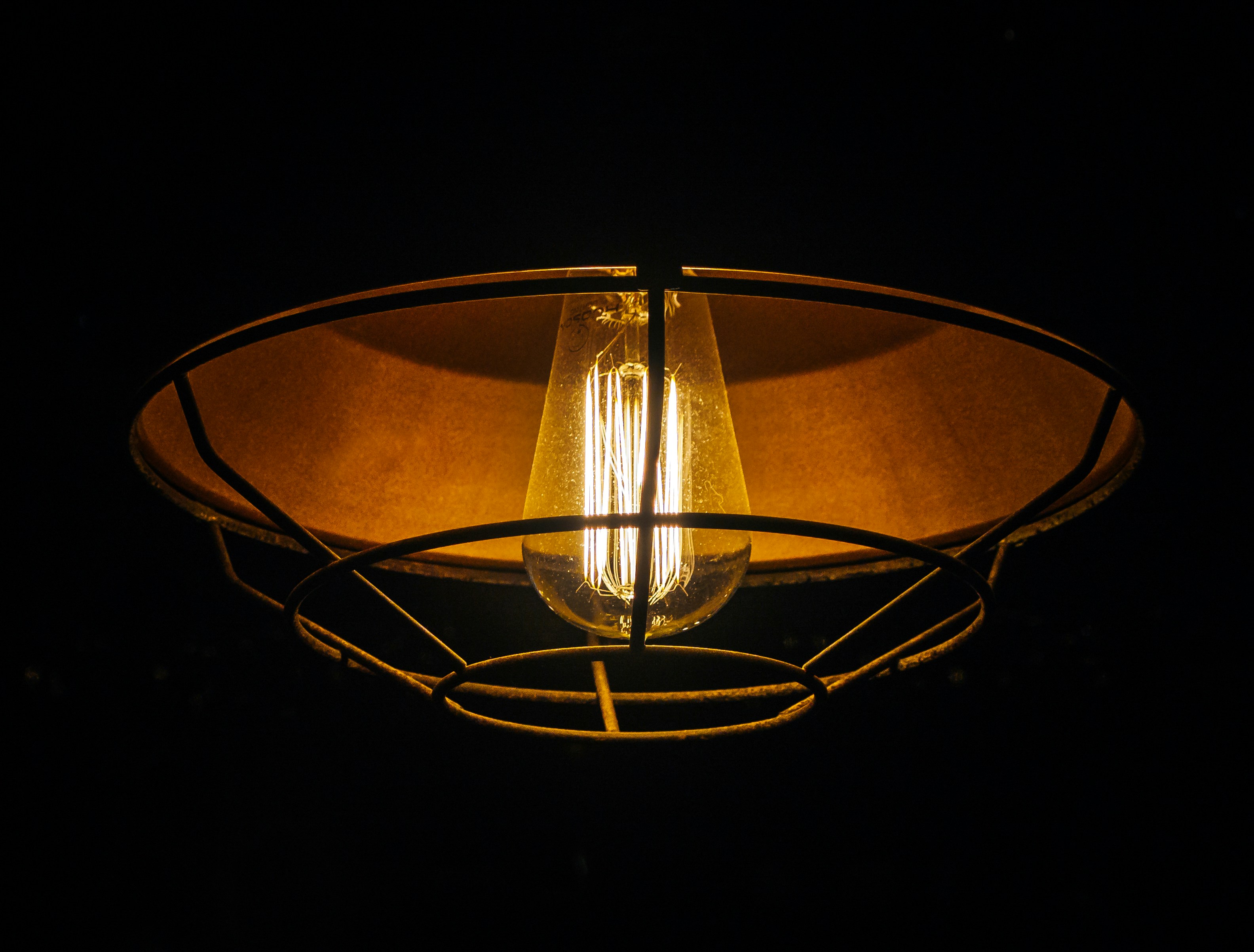 A vintage-style light fixture with a warm glow, showcasing a filament bulb encased in a decorative metal frame against a dark background.