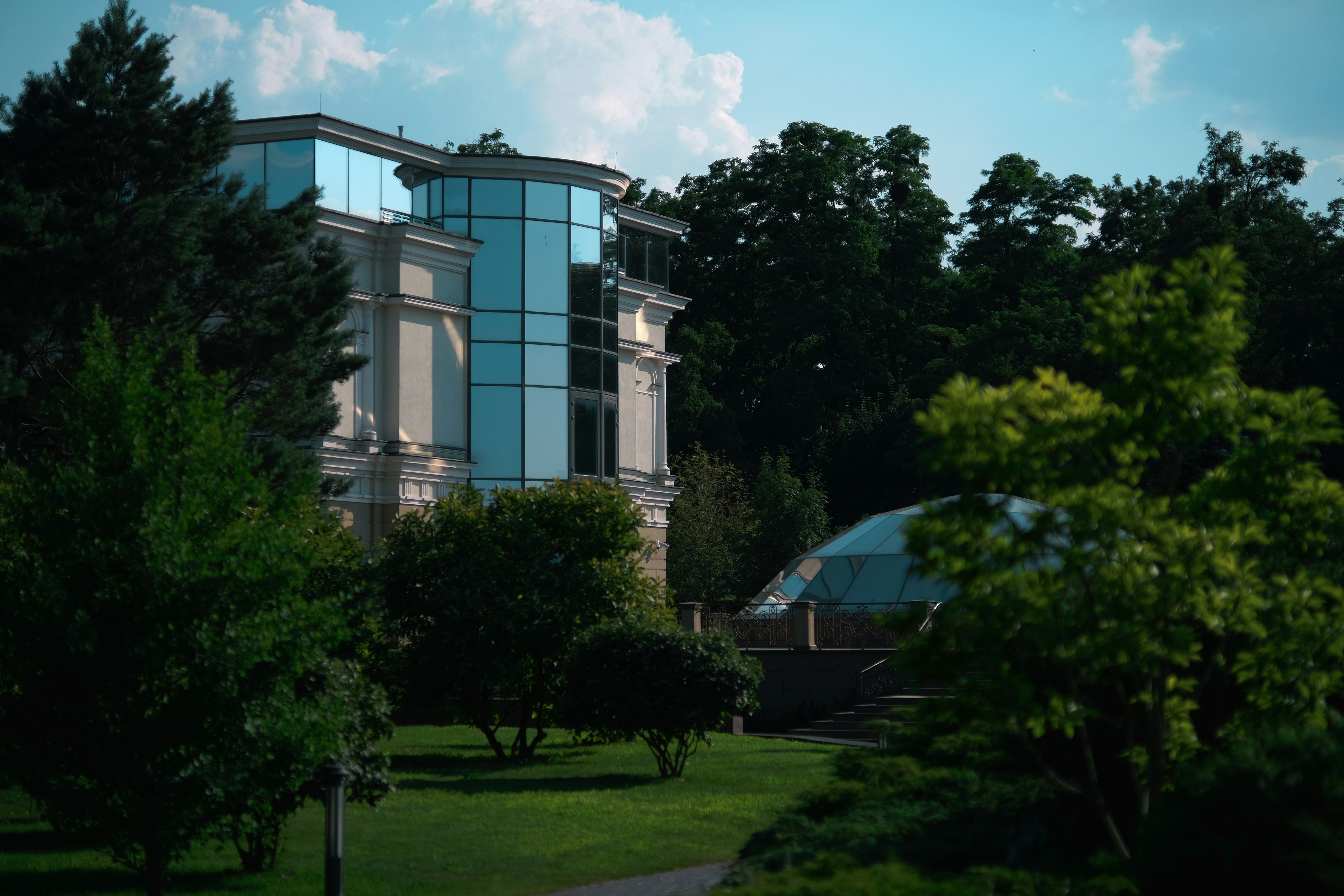Contemporary building with reflective glass facade surrounded by lush greenery and trees, showcasing a harmonious blend of architecture and nature.