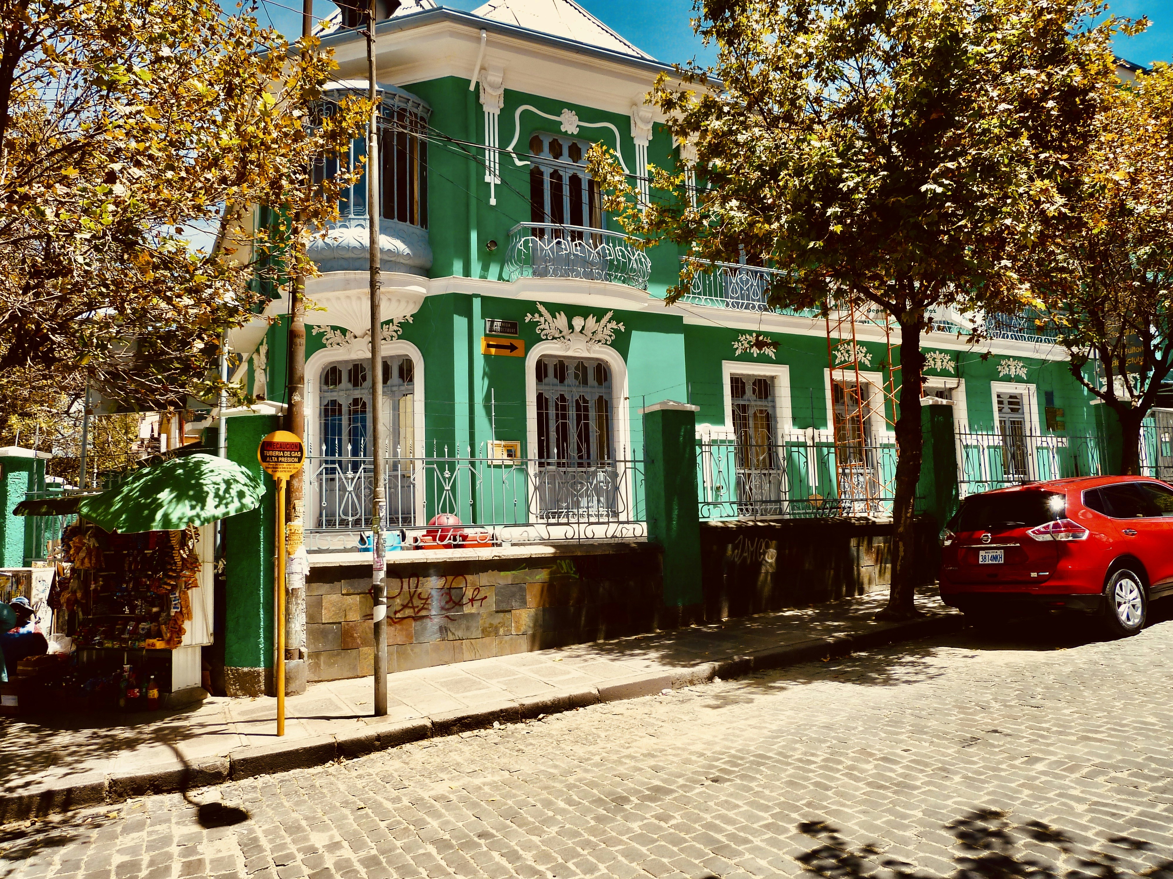Charming green building with ornate balconies and a red car parked on a sunlit cobblestone street.