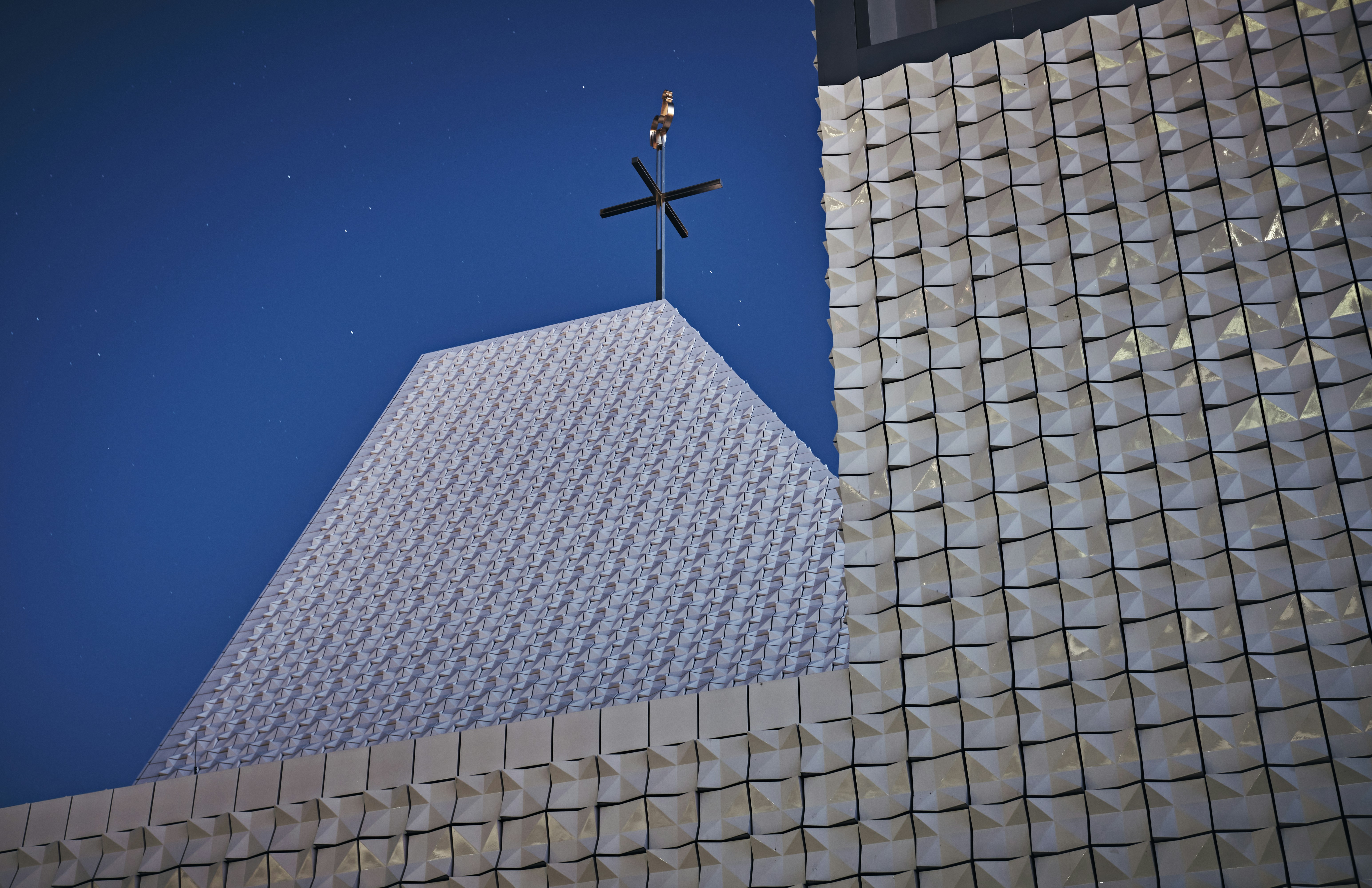 Cross atop a textured church facade under a clear blue sky