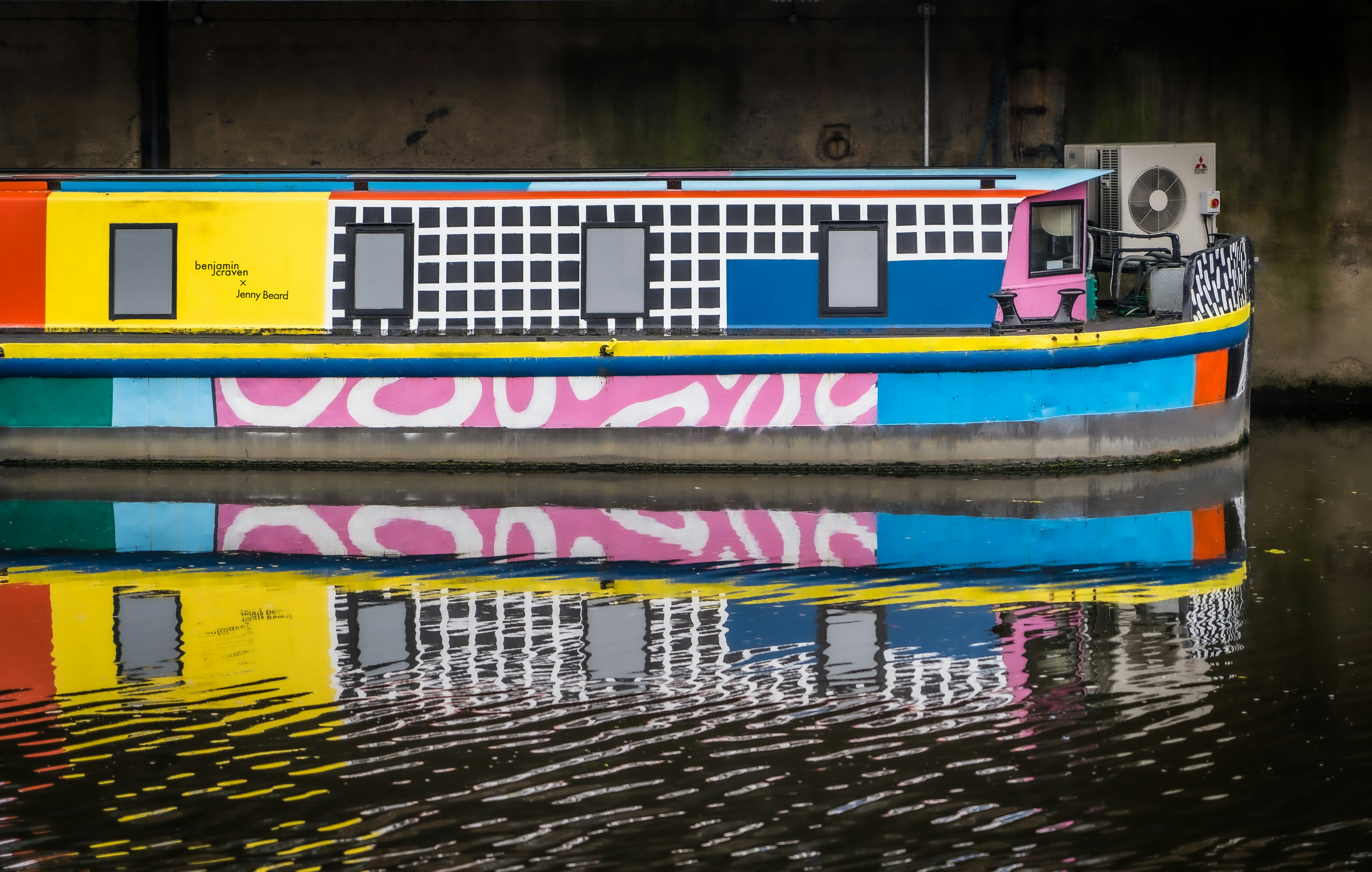 Colorful houseboat with geometric patterns reflected in calm water.