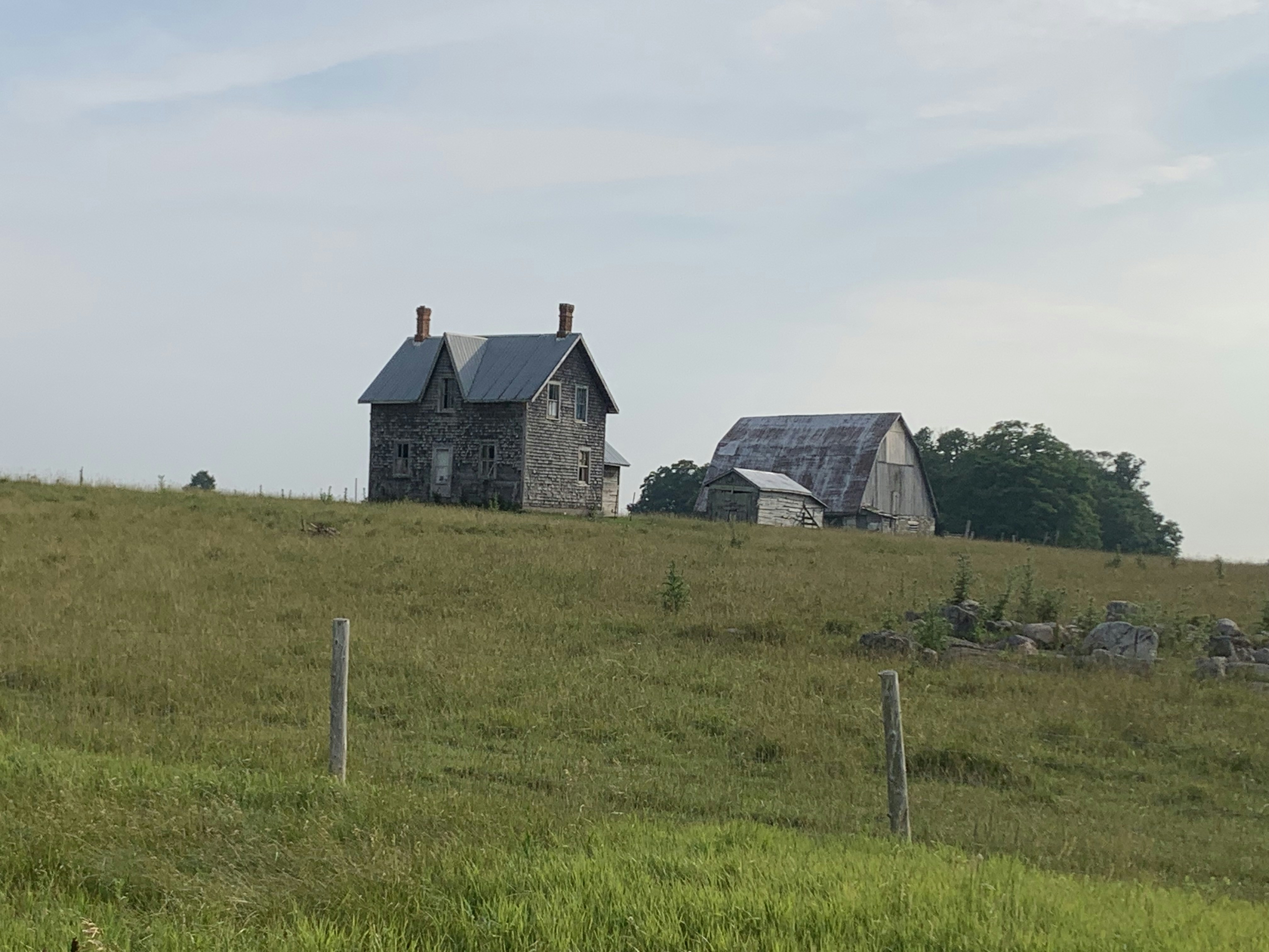 Weathered stone farmhouse and barn stand amidst lush green fields under a soft sky.