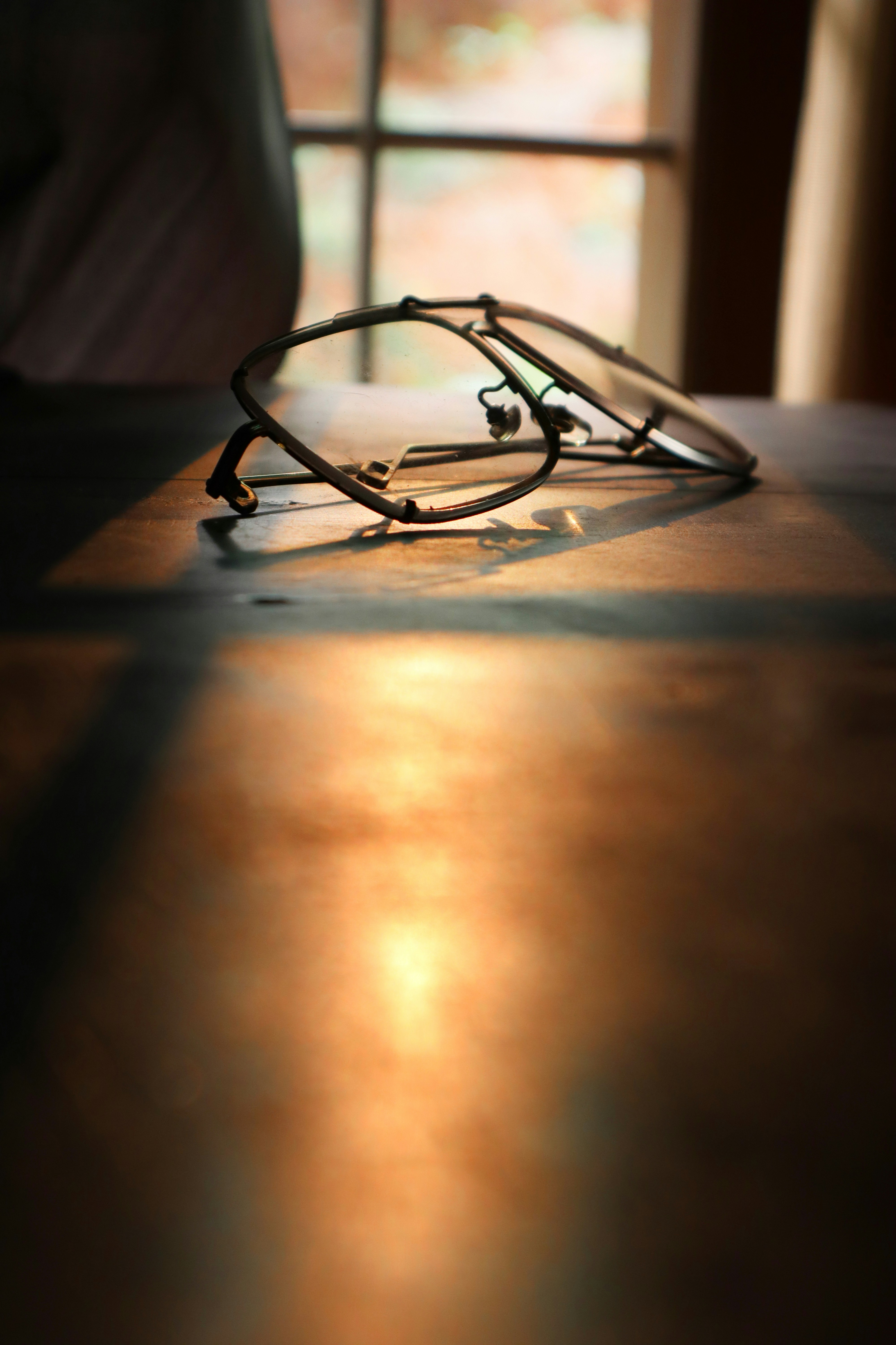 Lone spectacles in amber window light on a weathered wooden table