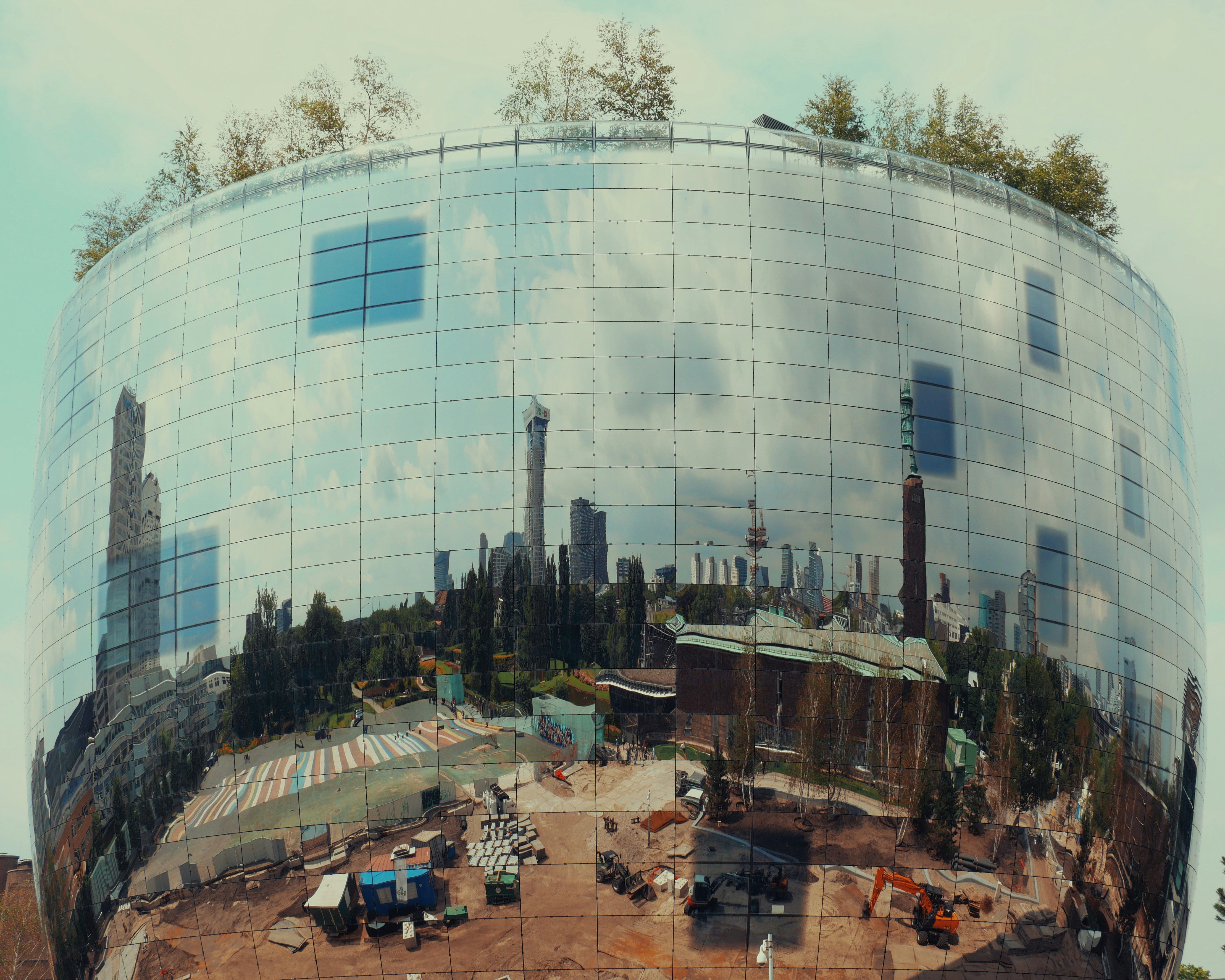 Curved glass building reflecting a distorted cityscape under a sky with scattered clouds.