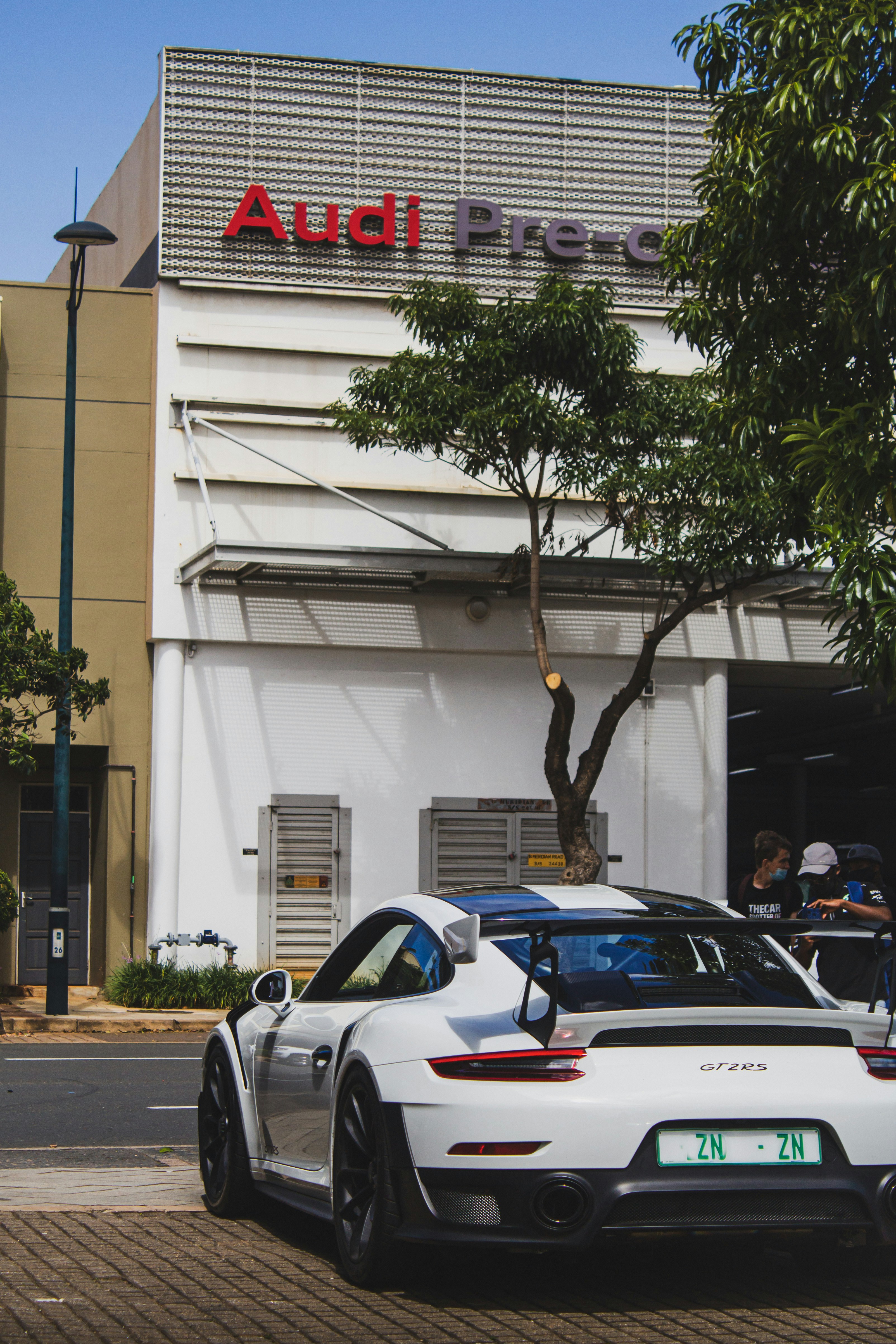 Rear-Quarter Glint: White Porsche Framed by an Audi Pre-owned Façade