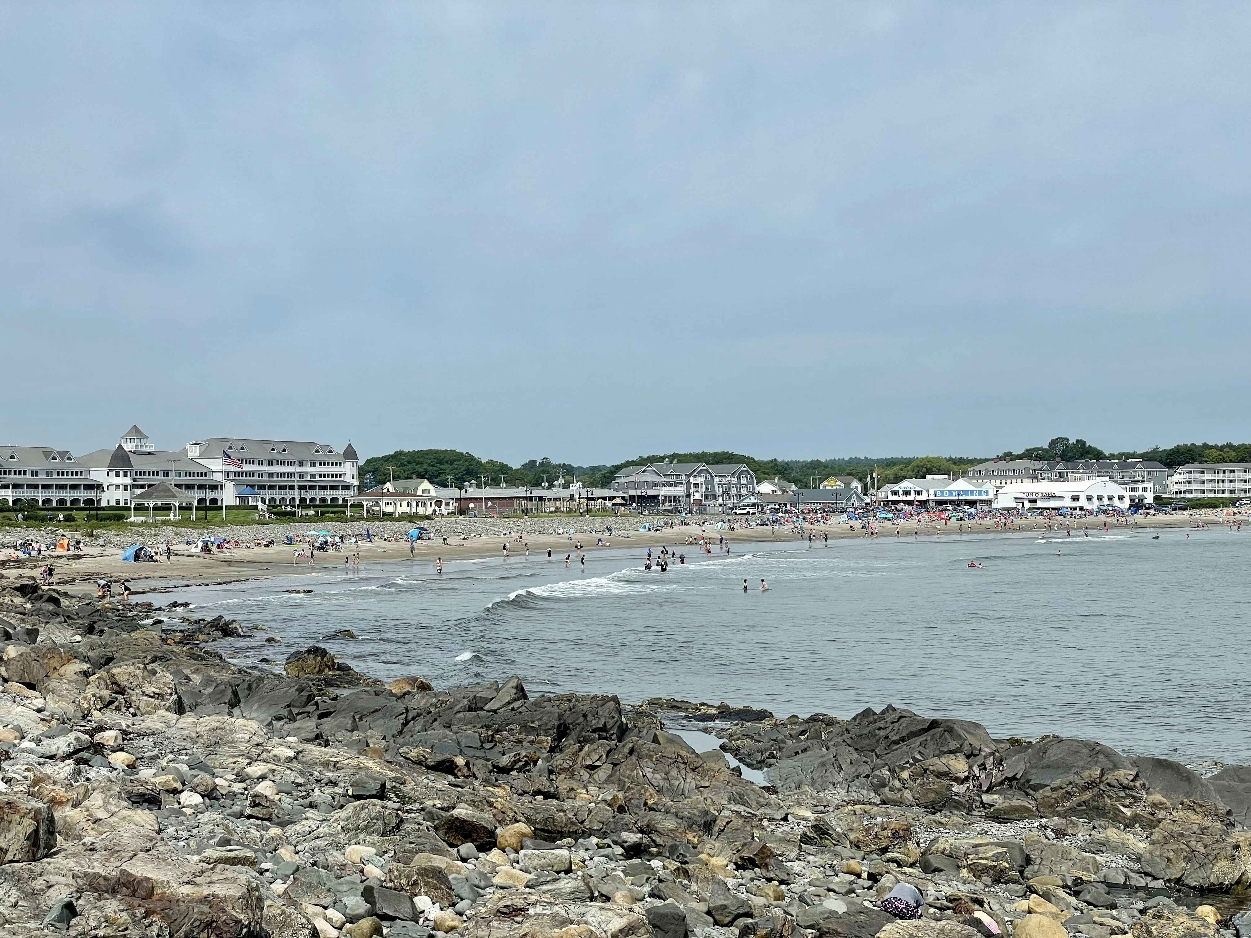Vibrant beach scene with families enjoying the sun and waves, framed by rocky shores and distant hotels. A perfect summer getaway.