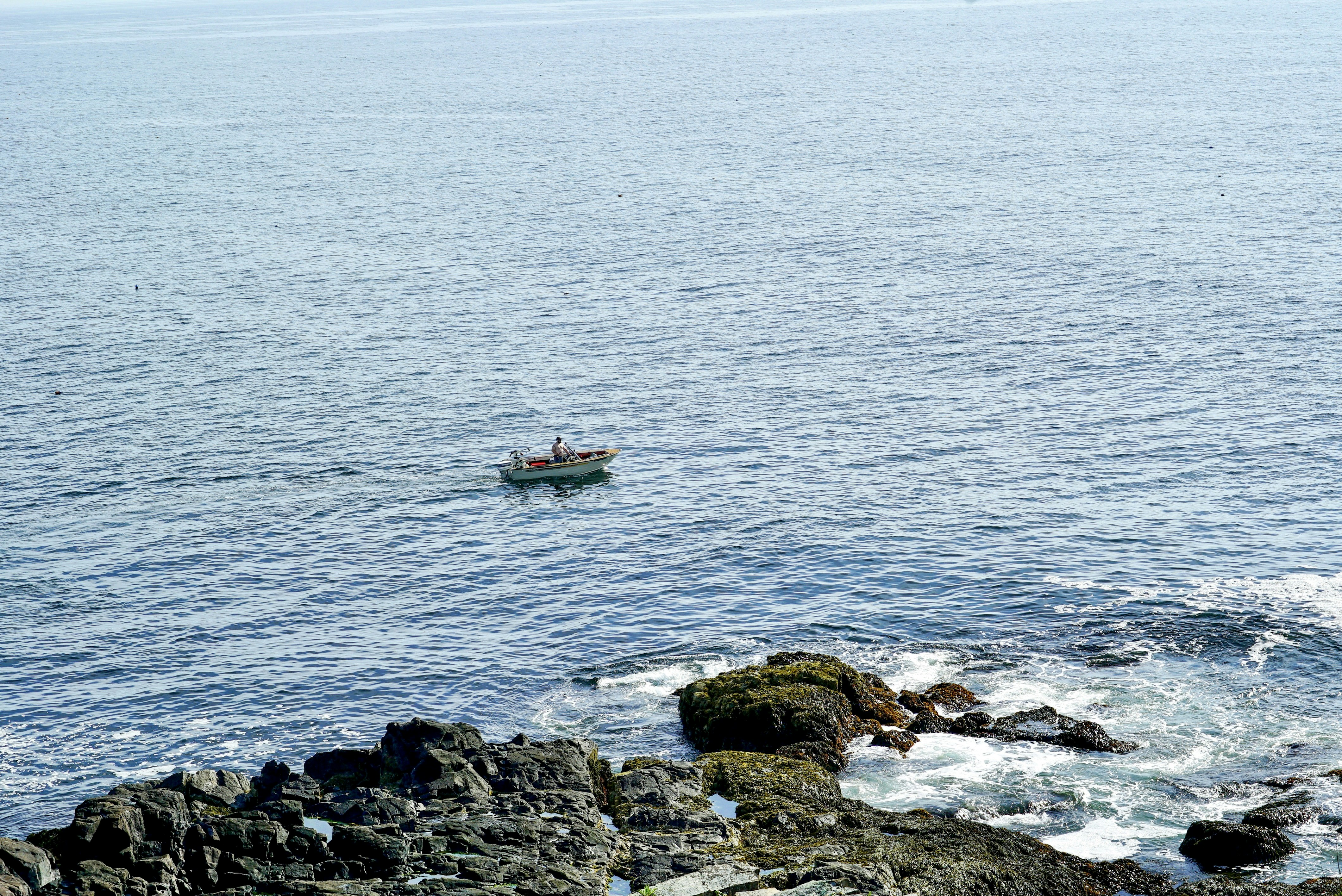 A small fishing boat navigates the tranquil sea, surrounded by rugged coastal rocks and gentle waves.