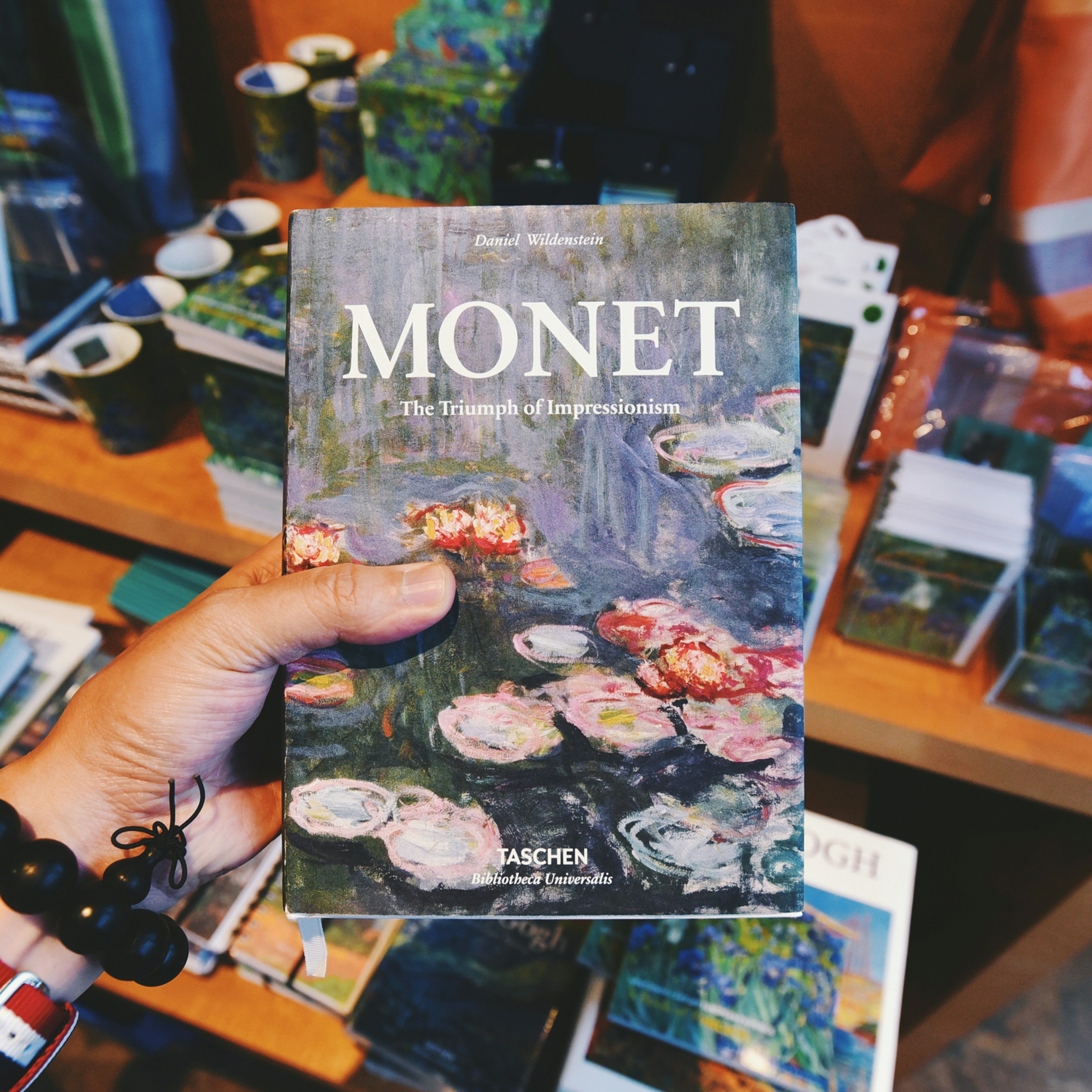 Handful of Monet: A Book Held Aloft in a Colorful Retail Scene