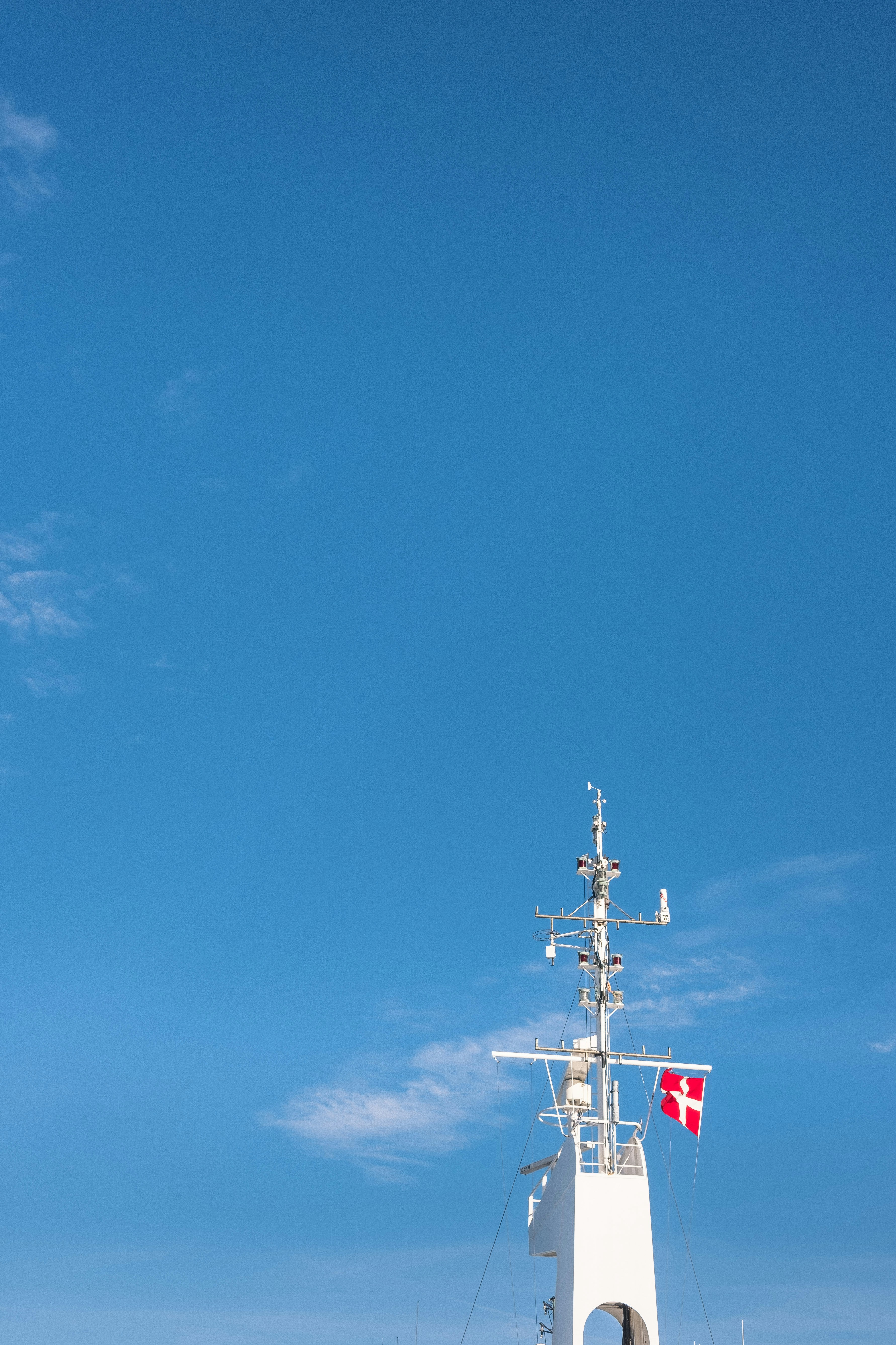 White ship mast adorned with a Danish flag against a vibrant blue sky.