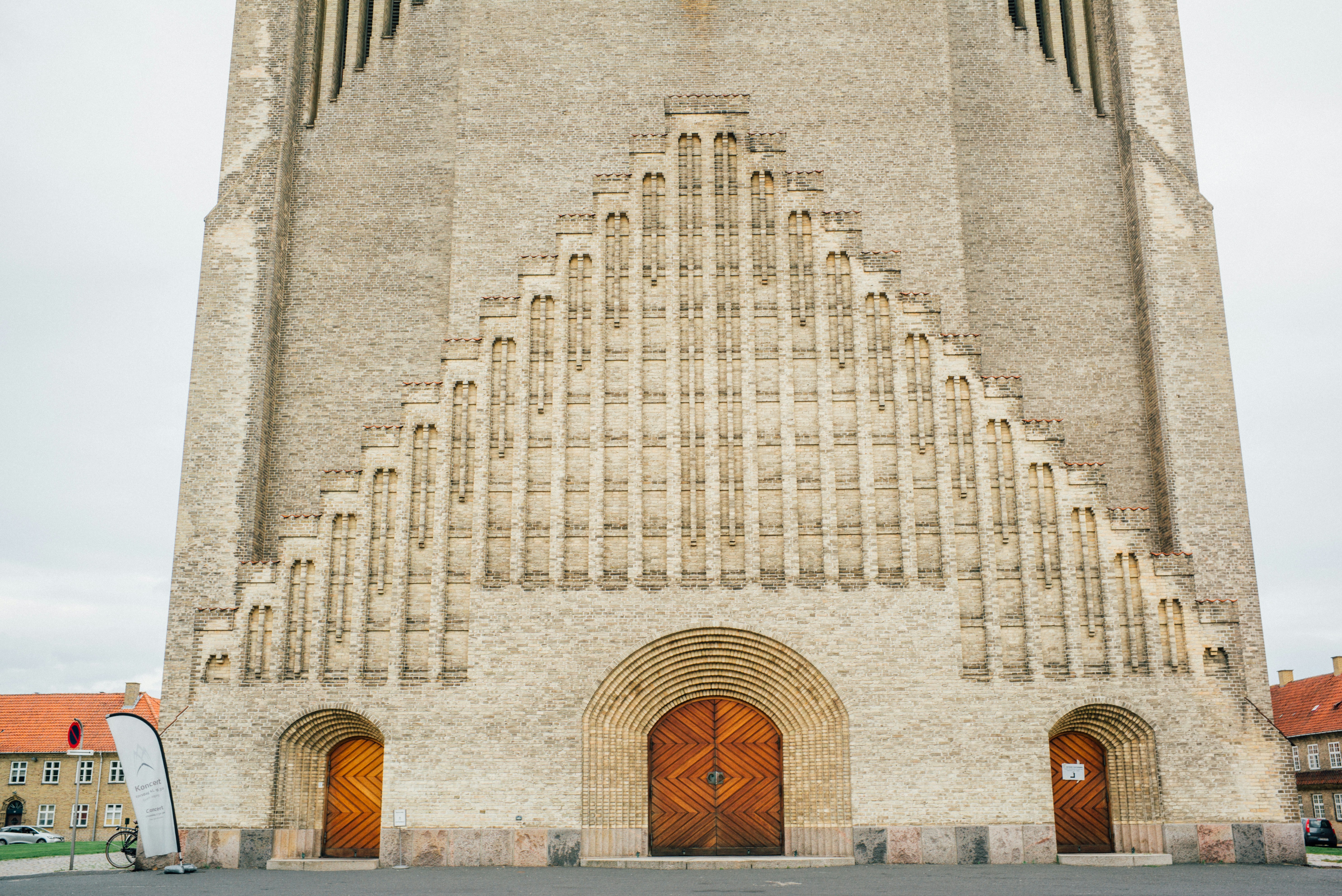 Geometric façade of a brick structure featuring intricate patterns and wooden doors. The design showcases a blend of modernism and traditional elements.