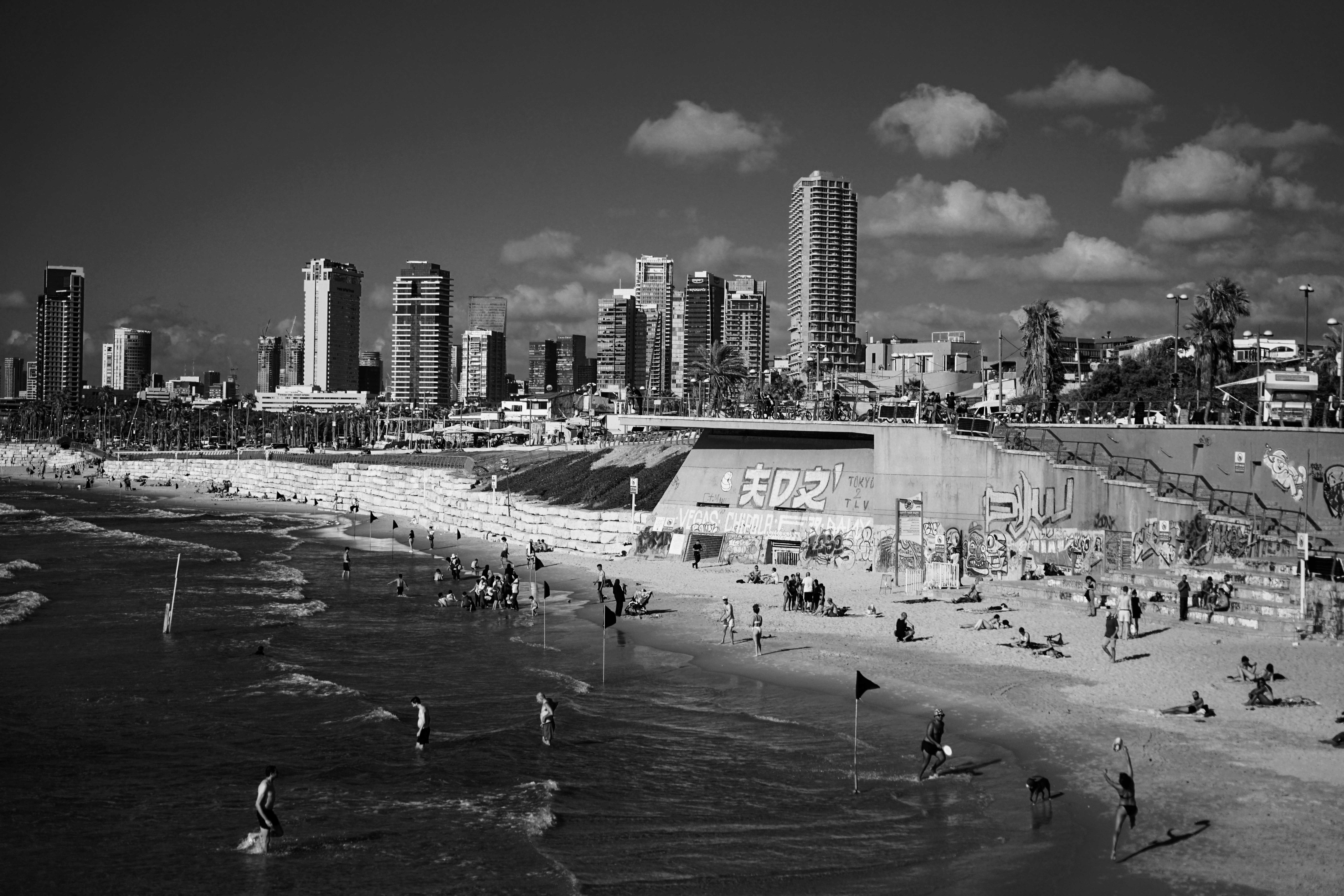 Coastal scene featuring a bustling beach with people enjoying the water, framed by a vibrant city skyline in the background.