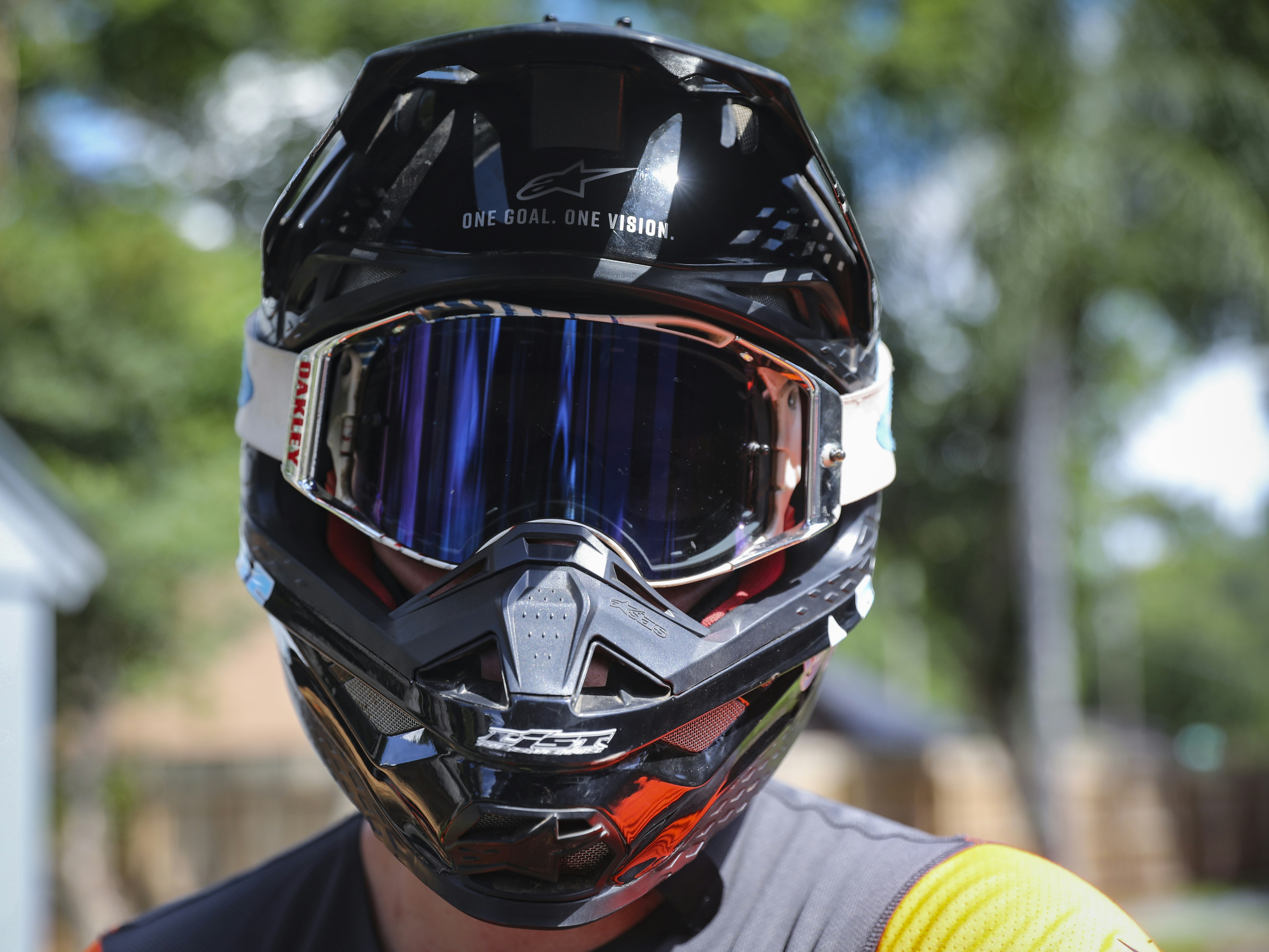 Close-up of a motocross rider wearing a helmet and goggles, showcasing the intricate design and reflective lenses. The background hints at an outdoor setting.