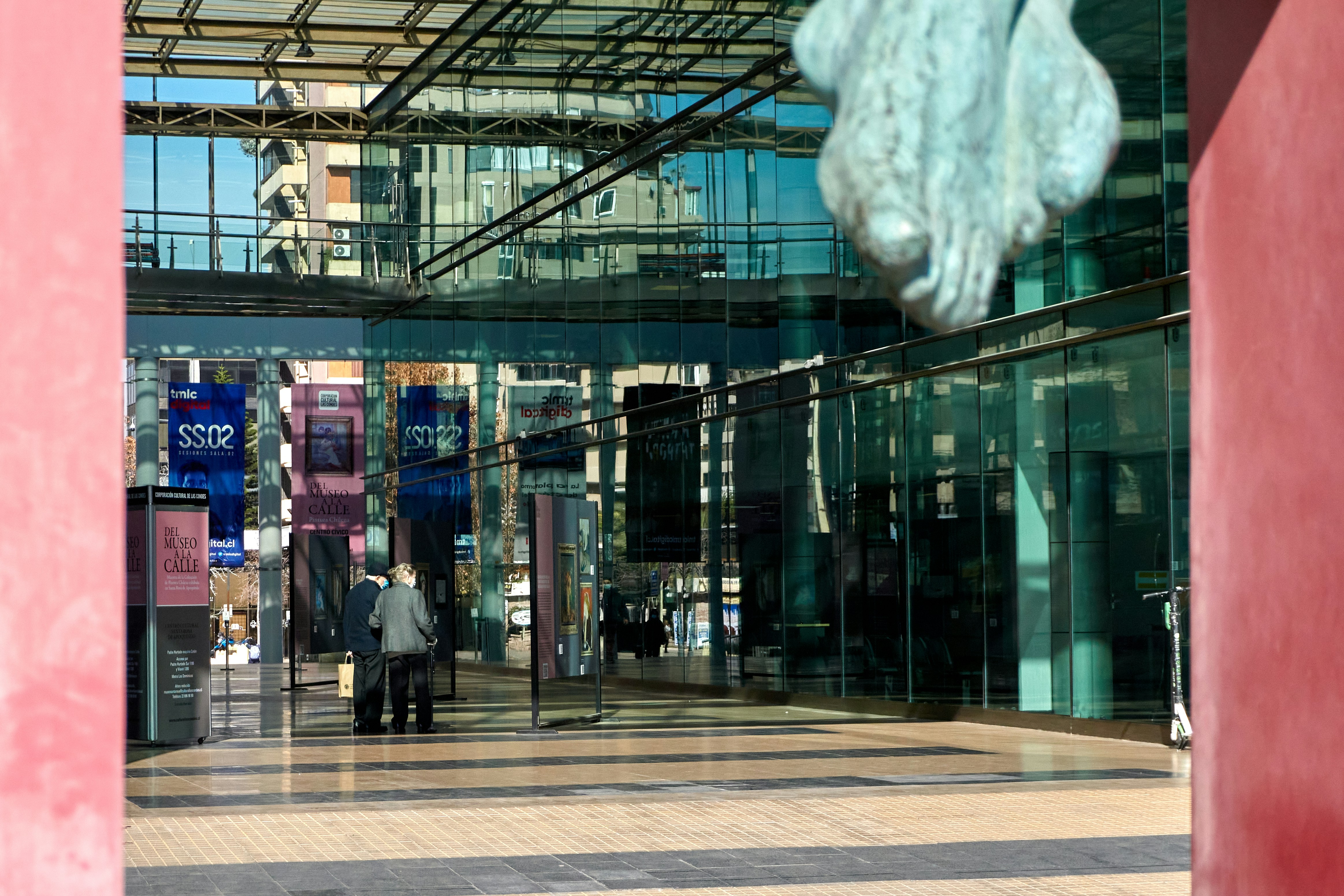 Ribboned Glass Portal: Two Visitors in a Modern Atrium Framed by a Sculptural Foreground