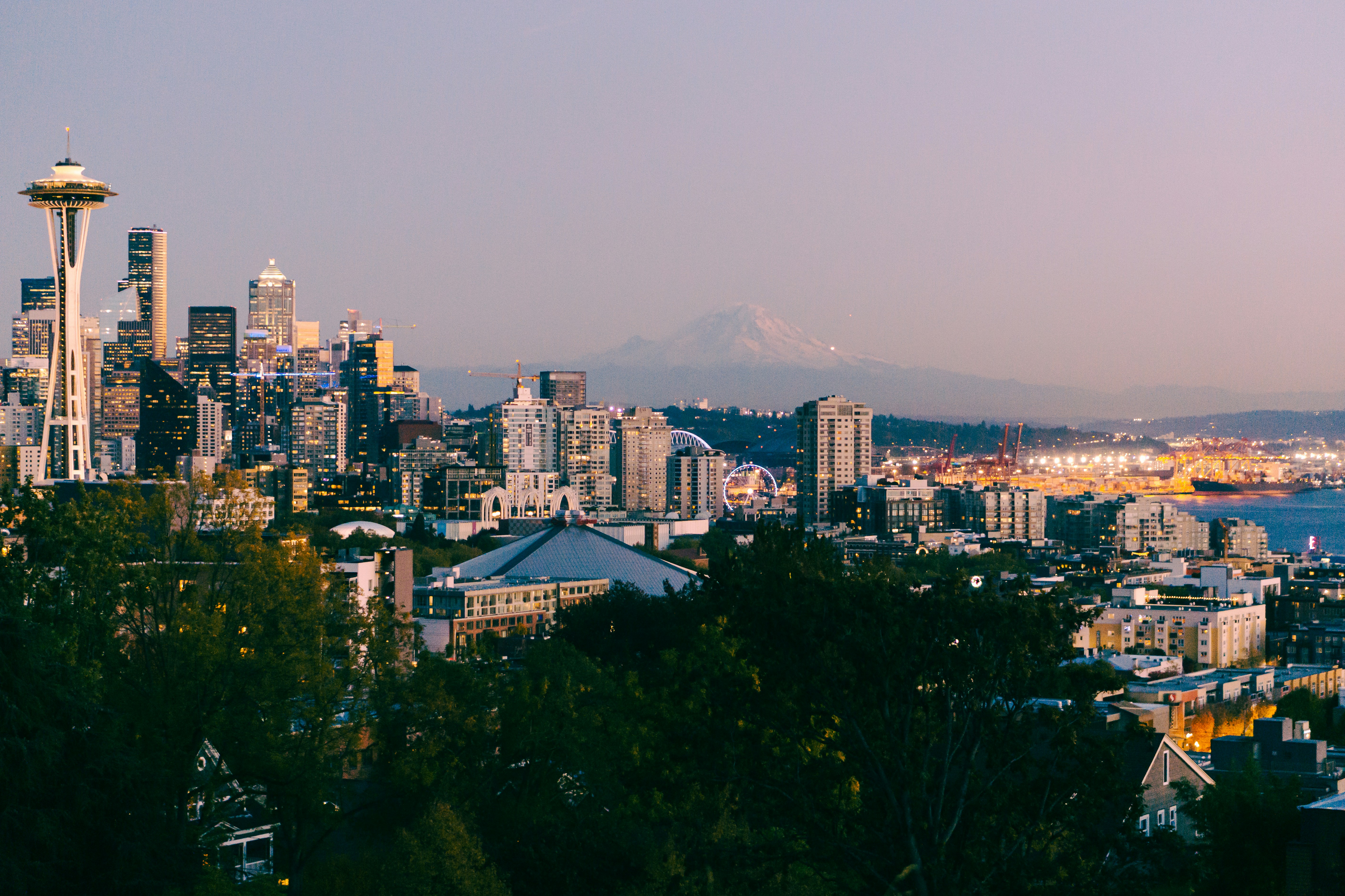 Seattle skyline illuminated at dusk, with Mount Rainier visible in the background and a vibrant cityscape reflecting on the water.