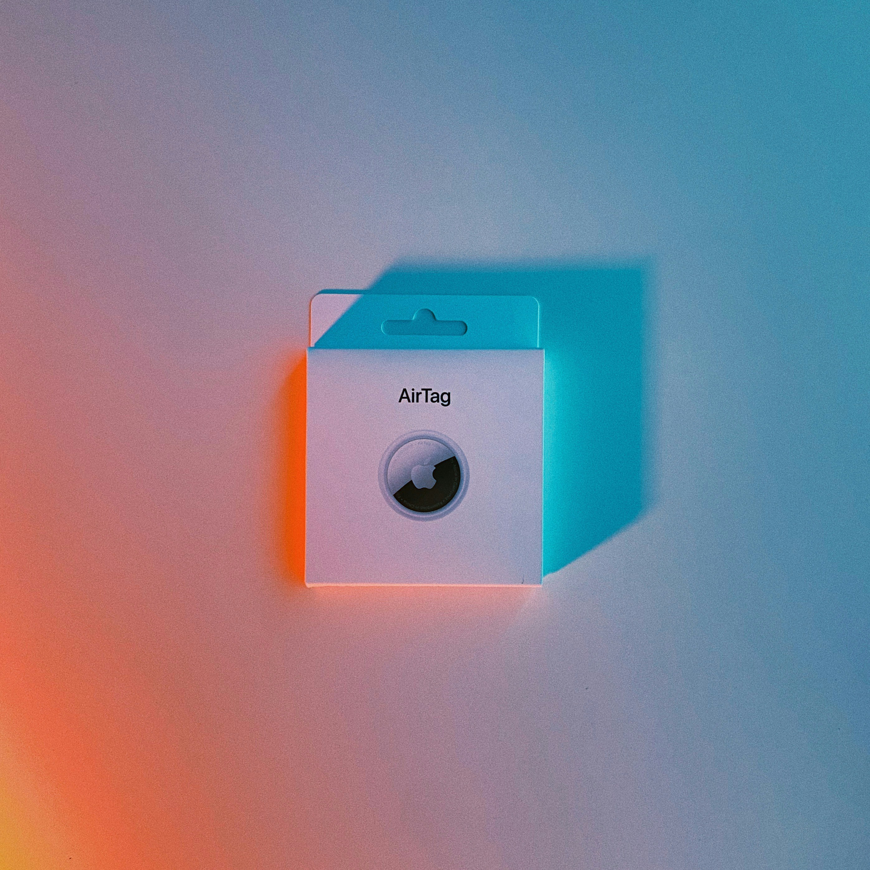 Apple AirTag packaging displayed against a gradient background, highlighting its sleek design and branding.