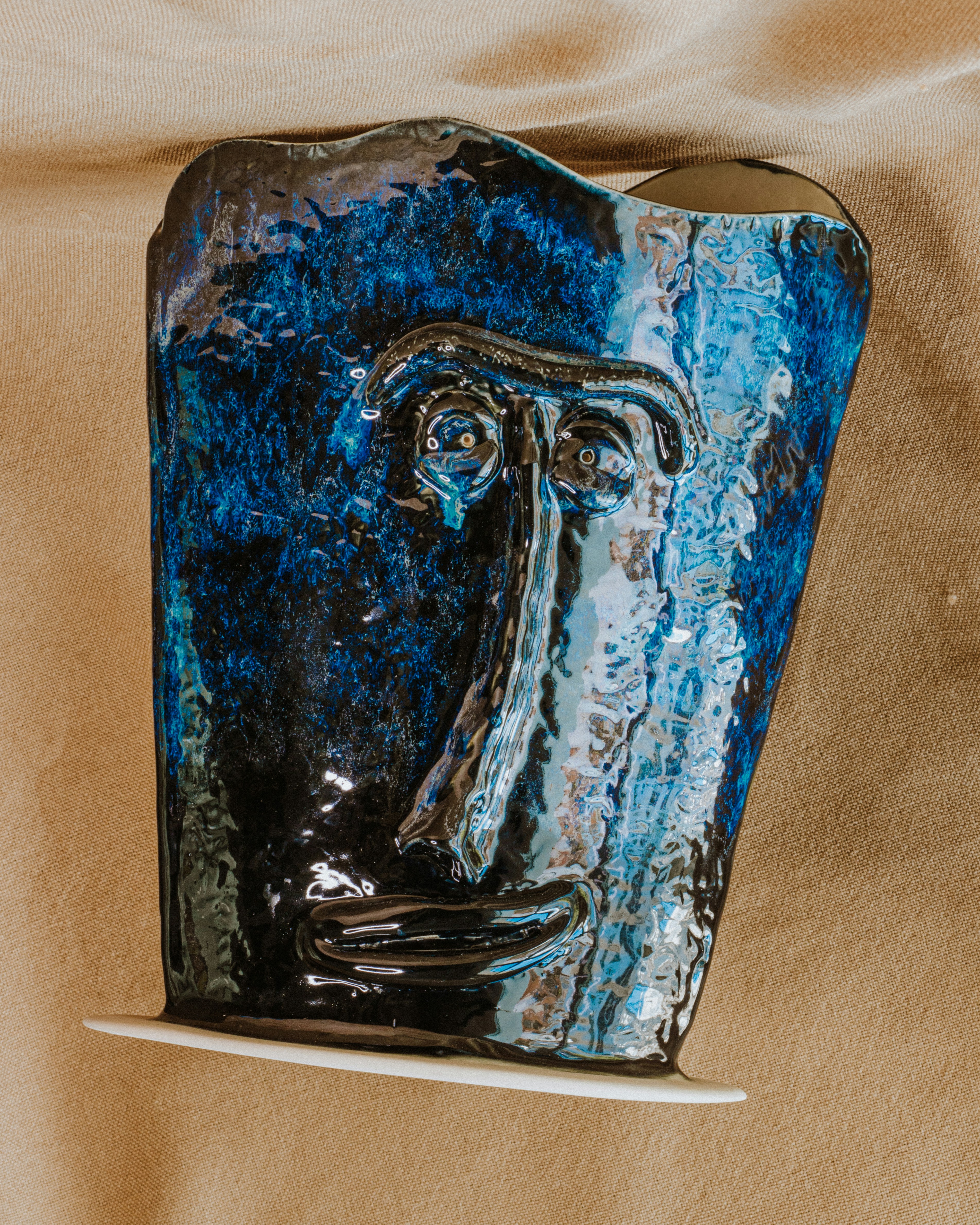Azure Glass Face: A sculpted visage resting on sandy beige fabric
