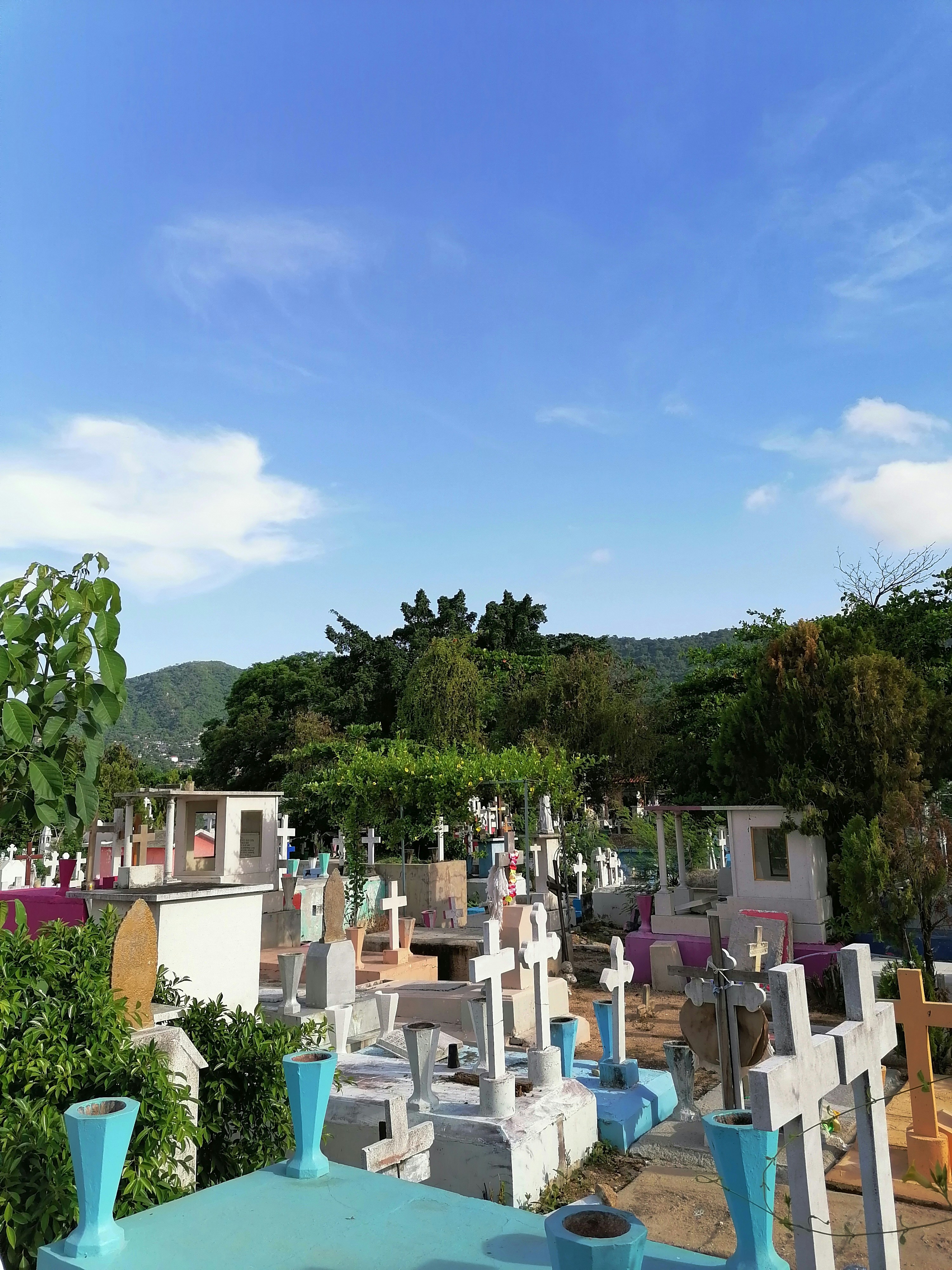 Colorful gravestones and crosses amidst lush greenery in a tranquil cemetery under a clear blue sky.