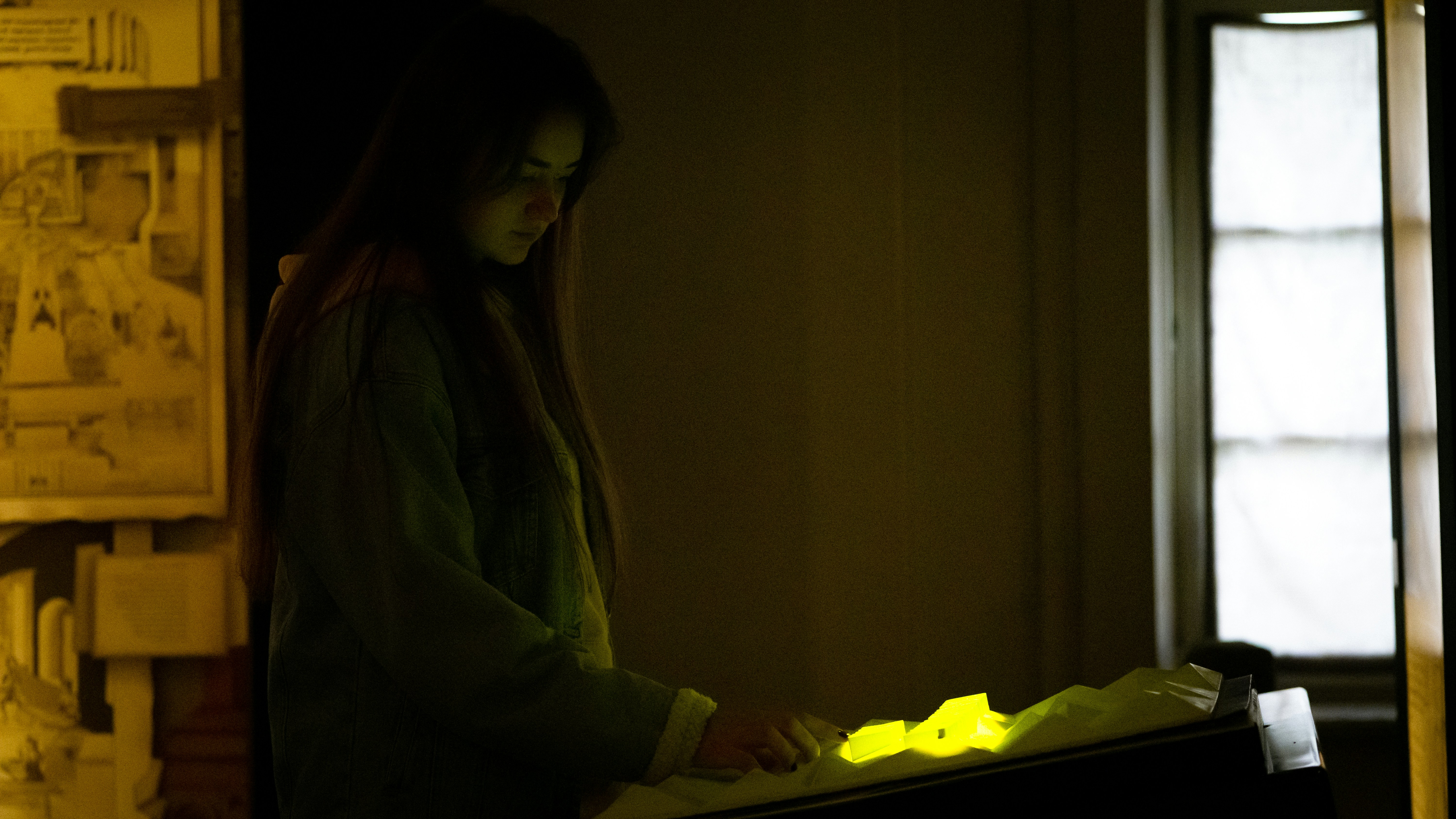 A young woman interacts with a glowing object in a dimly lit space, highlighting her engagement with the mysterious artifact.