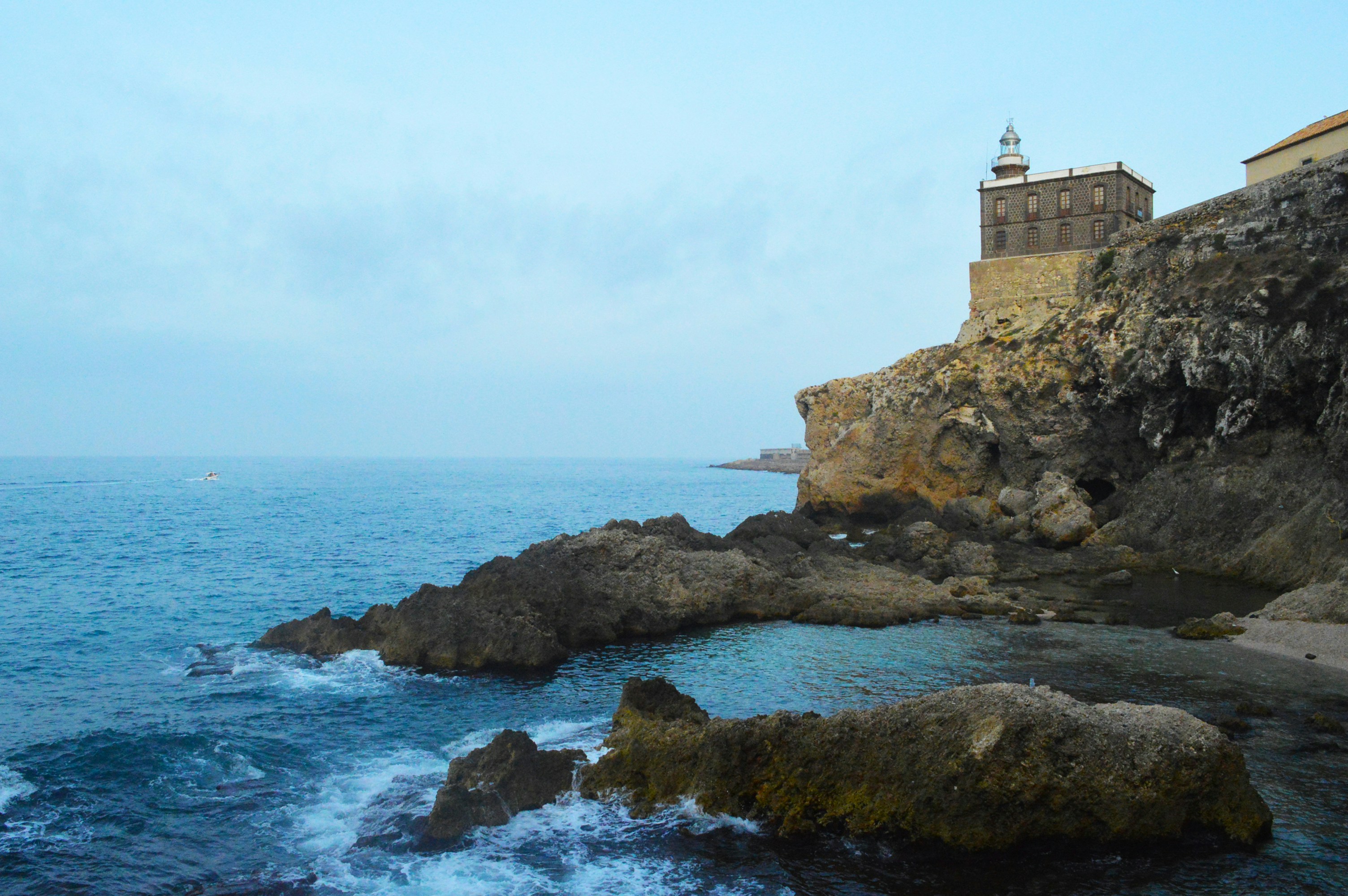 Brown concrete building on rock formation near sea during daytime photo ...