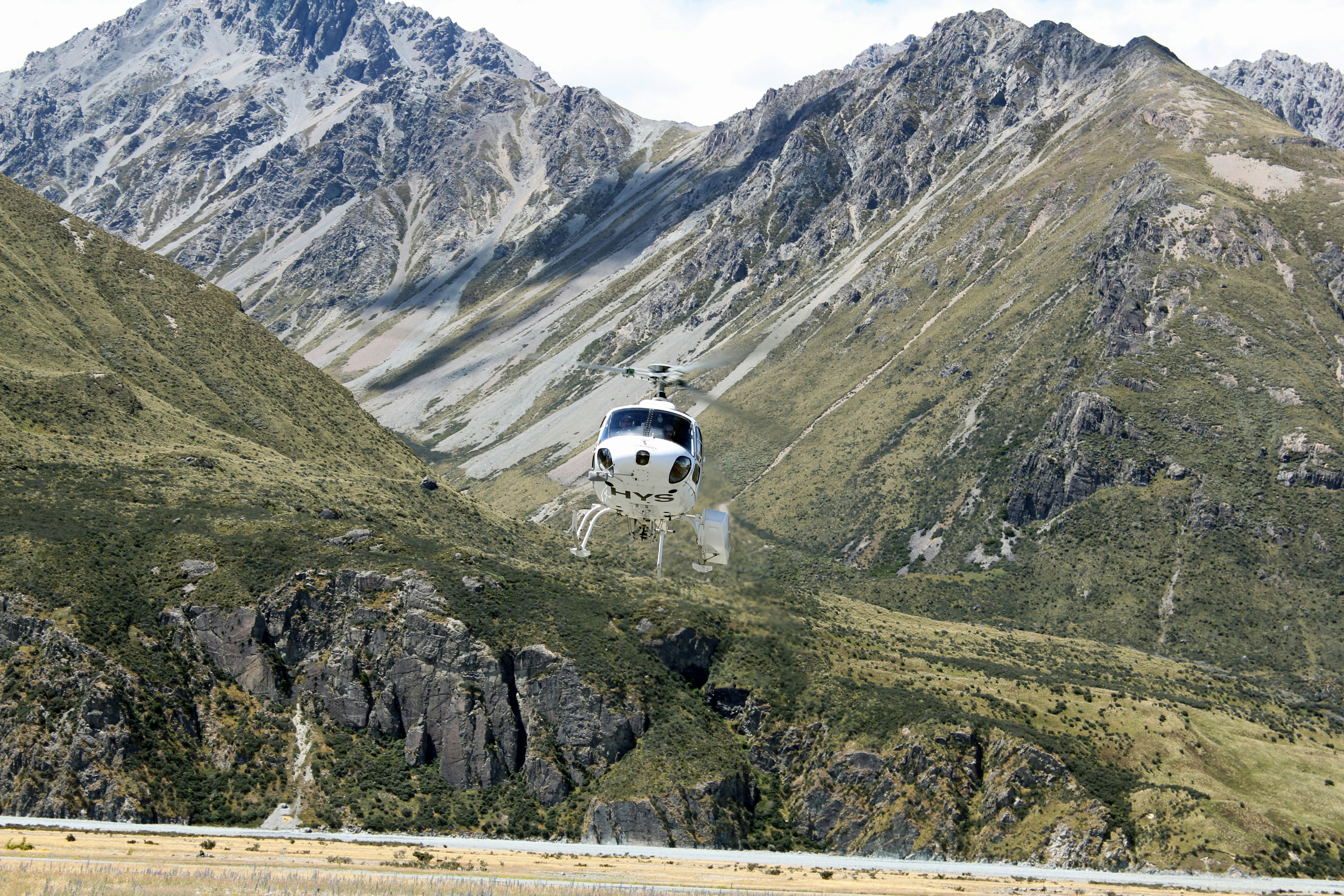 White helicopter gliding above a rugged Alpine saddle