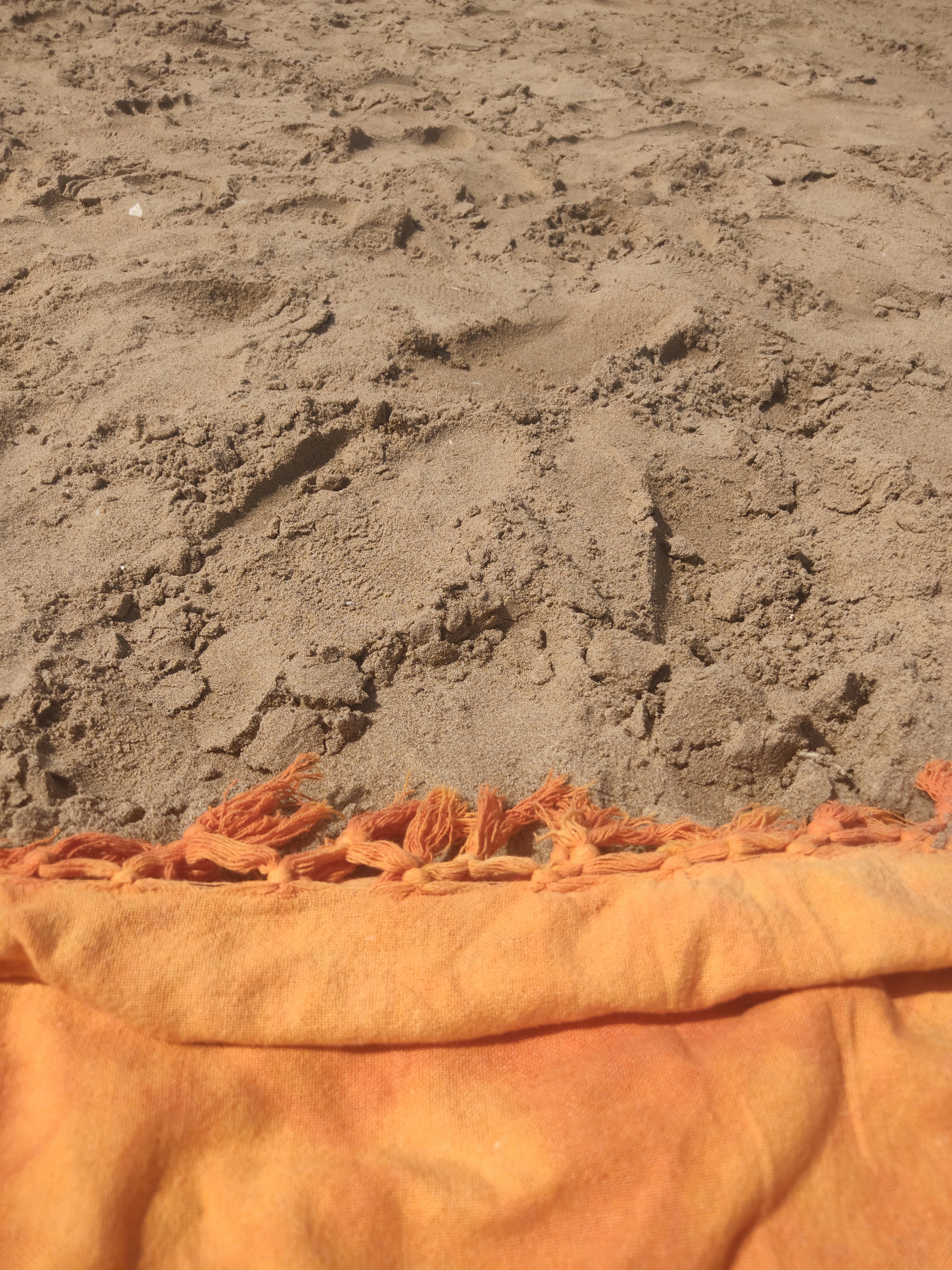Vibrant orange blanket resting on golden sandy beach, capturing the essence of relaxation and summer vibes.