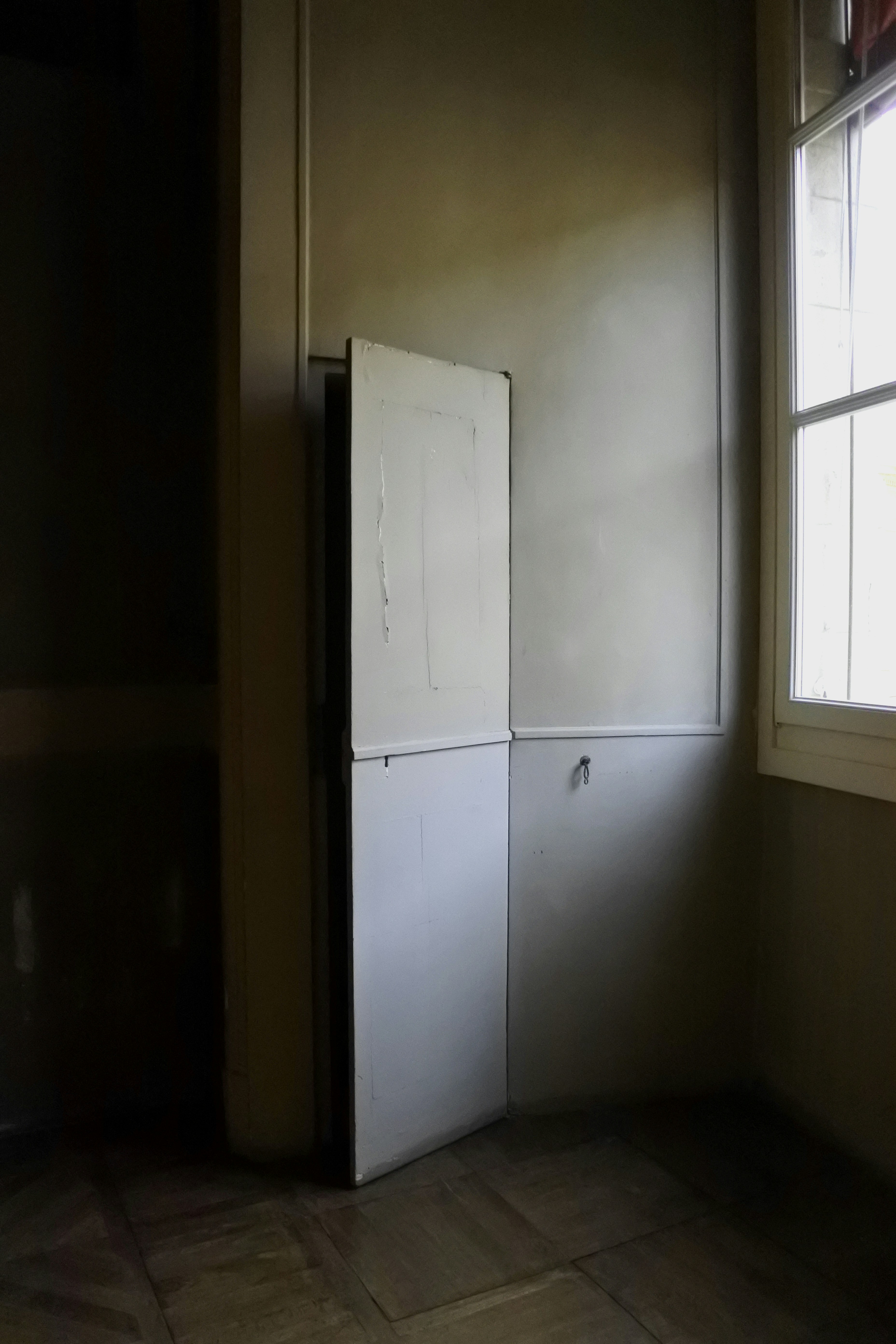 Narrow hallway with a partially open door illuminated by soft natural light from a window.