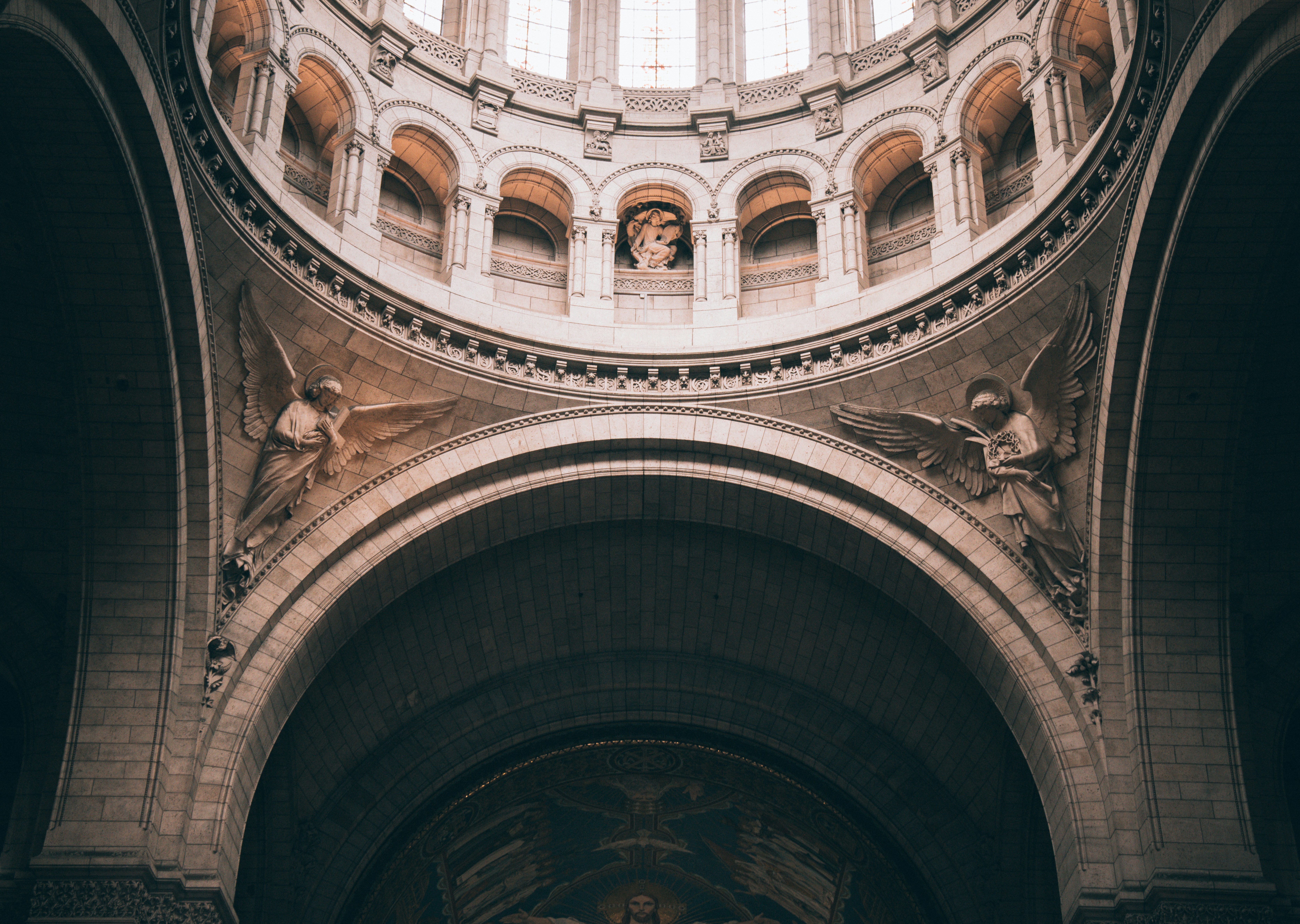 Intricate stone carvings of angels adorn the arches beneath a grand dome, showcasing remarkable architectural detail. The play of light enhances the ethereal atmosphere.