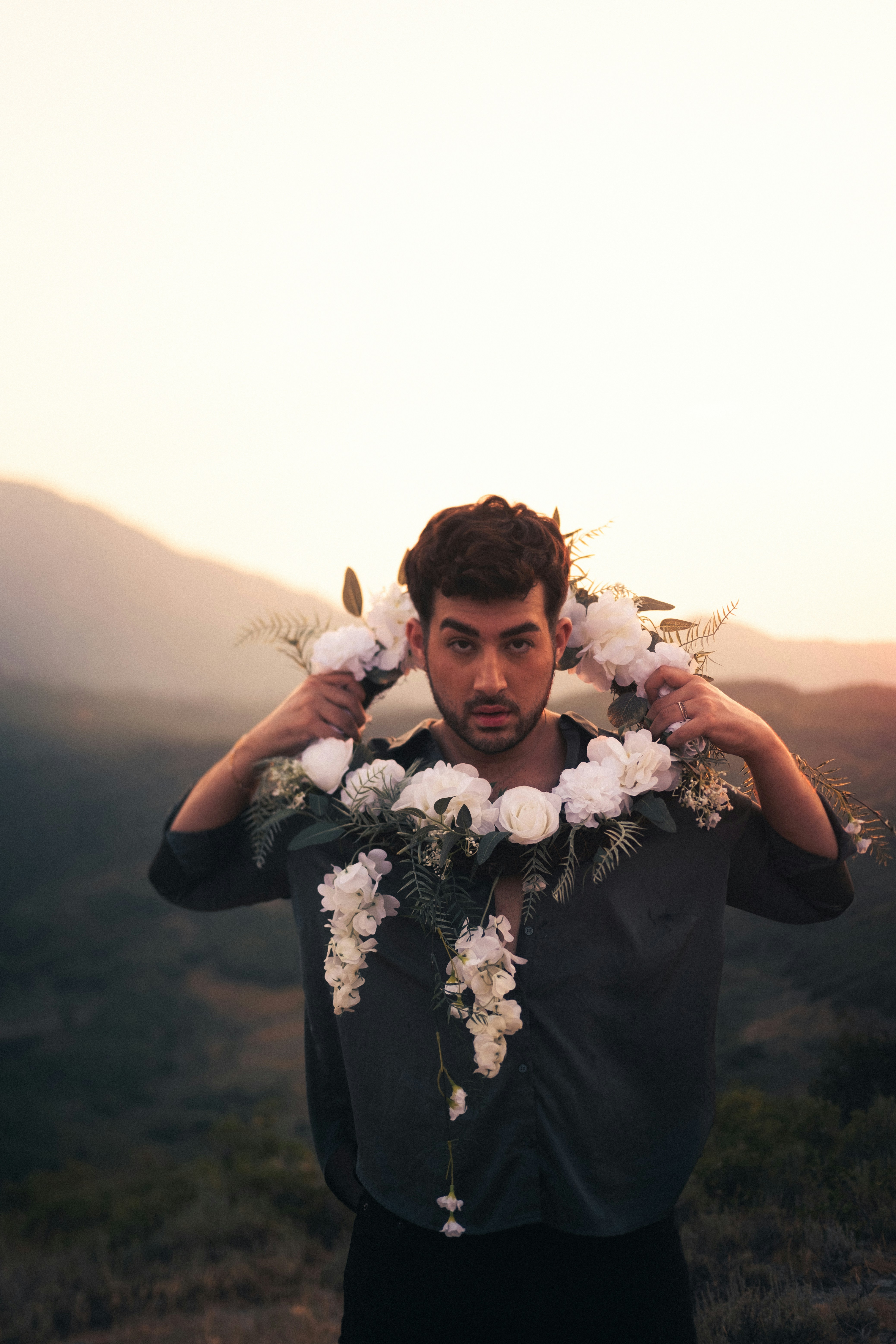 Dusk Crown Portrait: A Man with White Floral Garland Against a Golden Hillside
