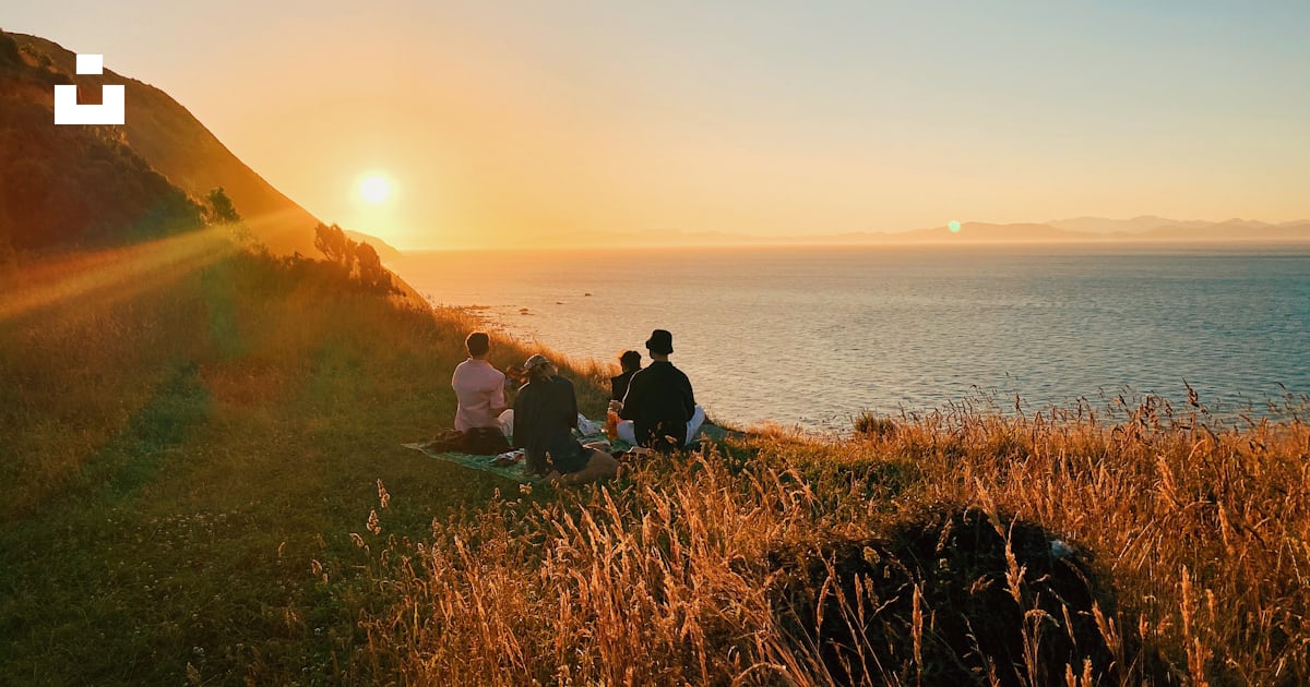2 Person Sitting On Green Grass Field Near Body Of Water During Sunset