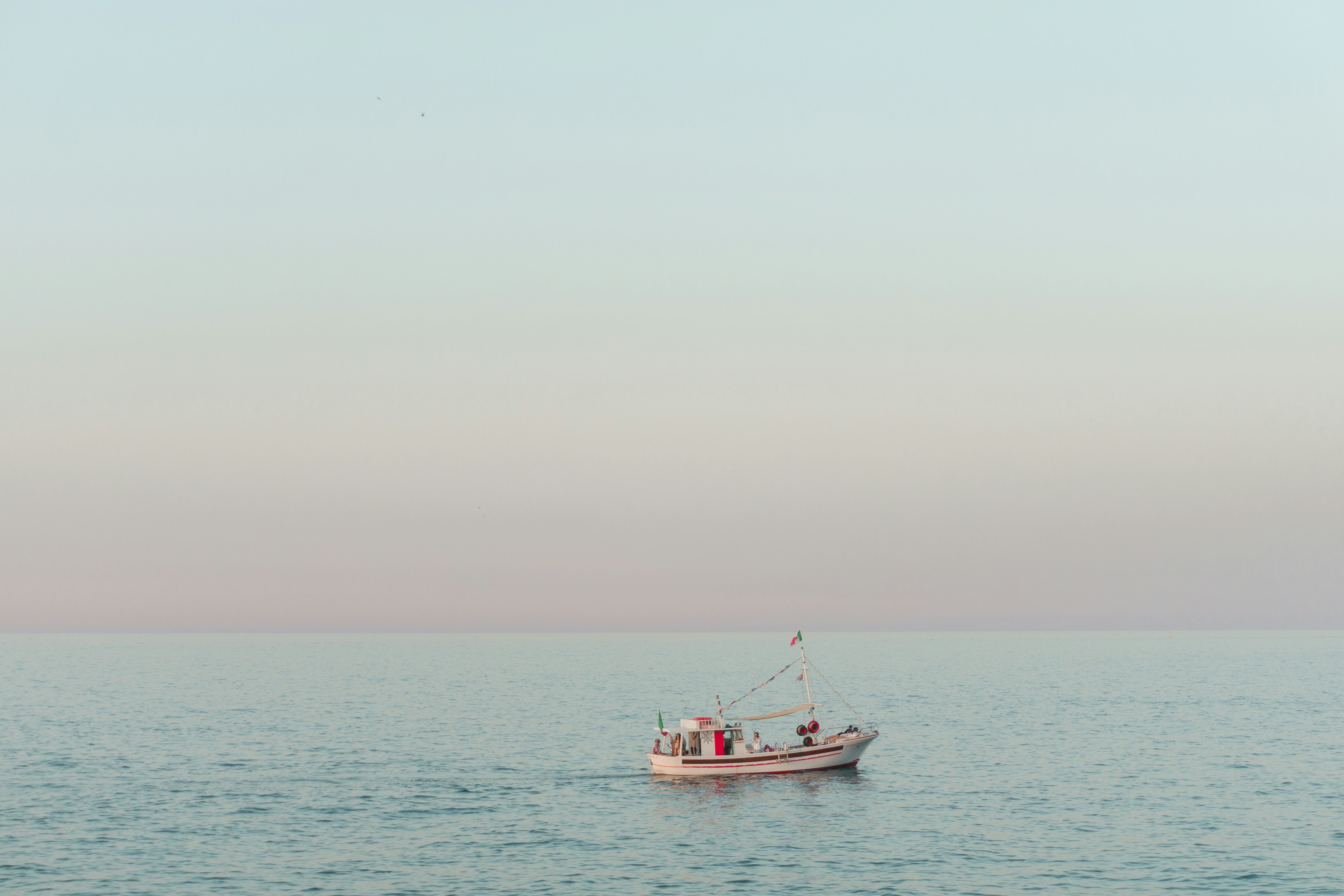 Red and white boat on calm sea under a pastel sky.