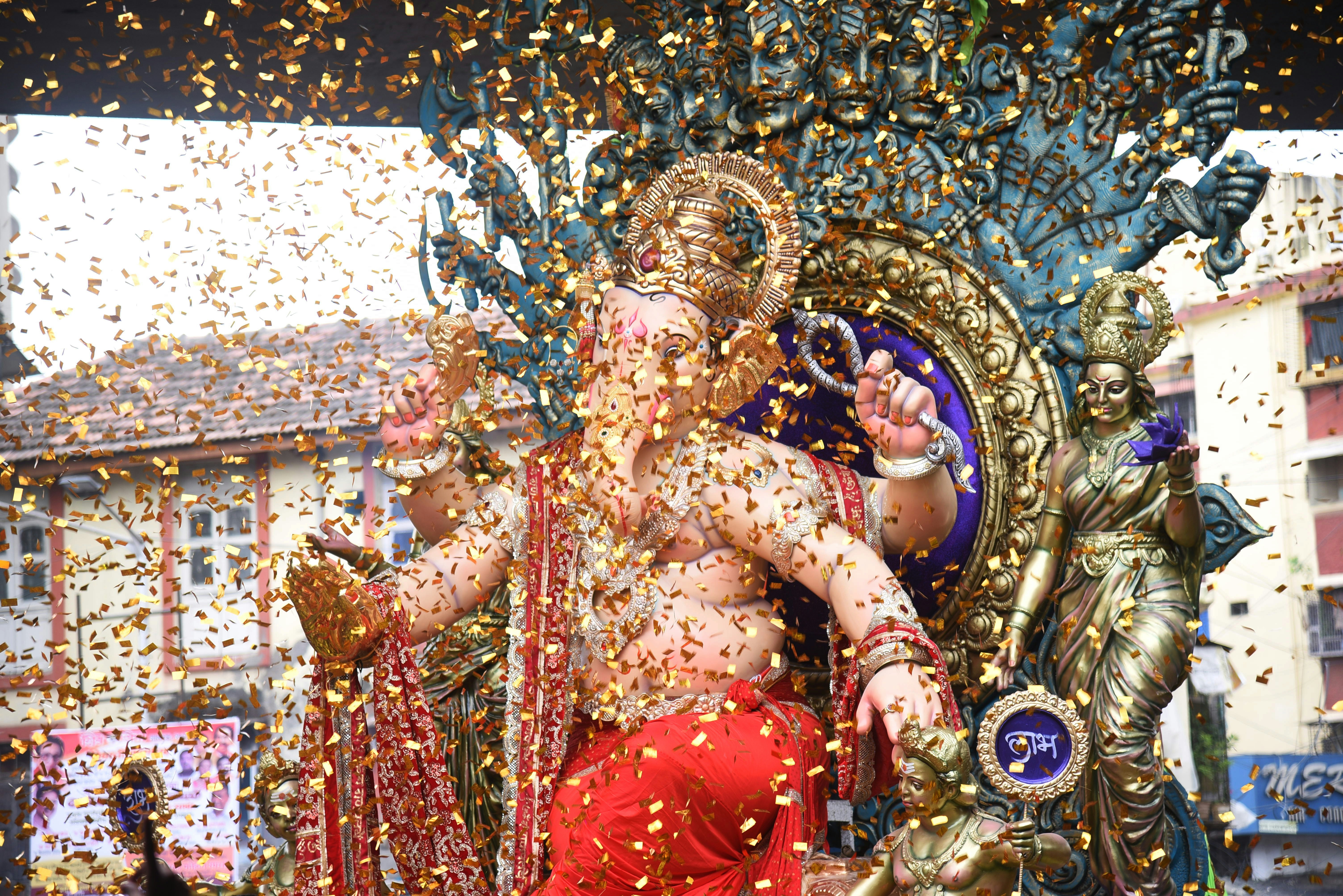 Colorful confetti showers over a majestic idol of Lord Ganesha, adorned with intricate decorations, during a festive celebration.