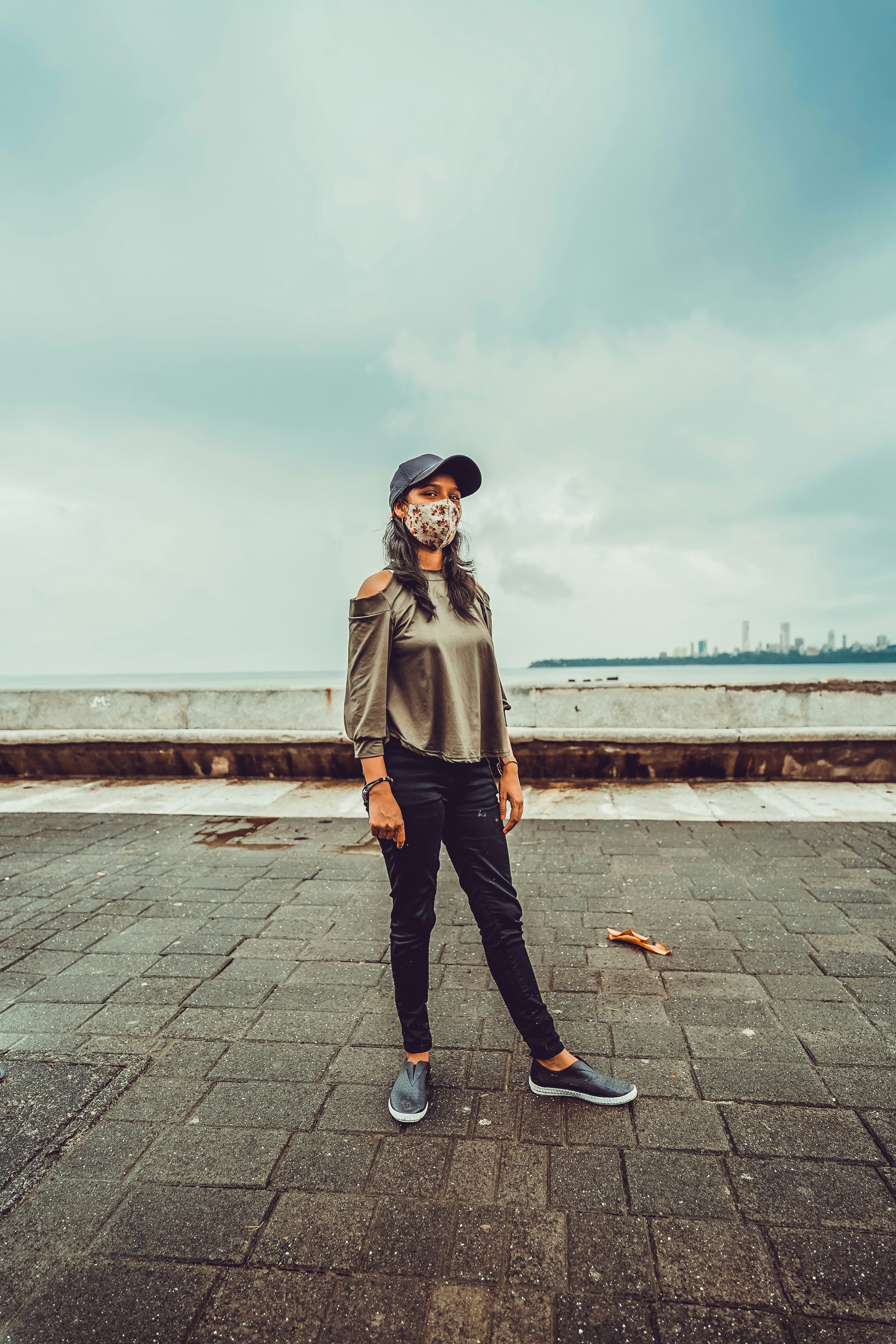 woman in gray coat and black pants standing on gray concrete pavement during daytime