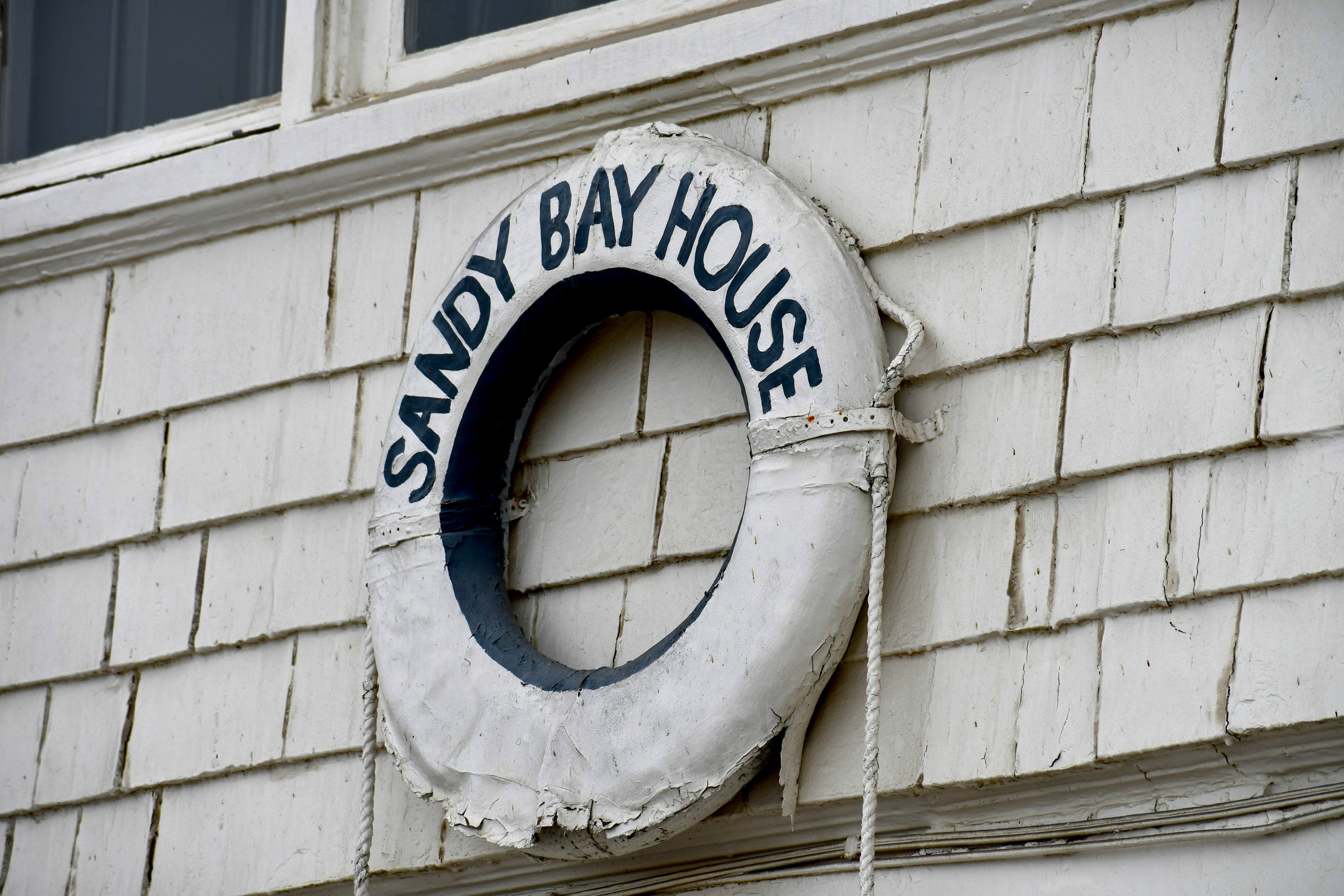 Lifebuoy with 'SANDY BAY HOUSE' inscribed, mounted on a weathered wooden wall.