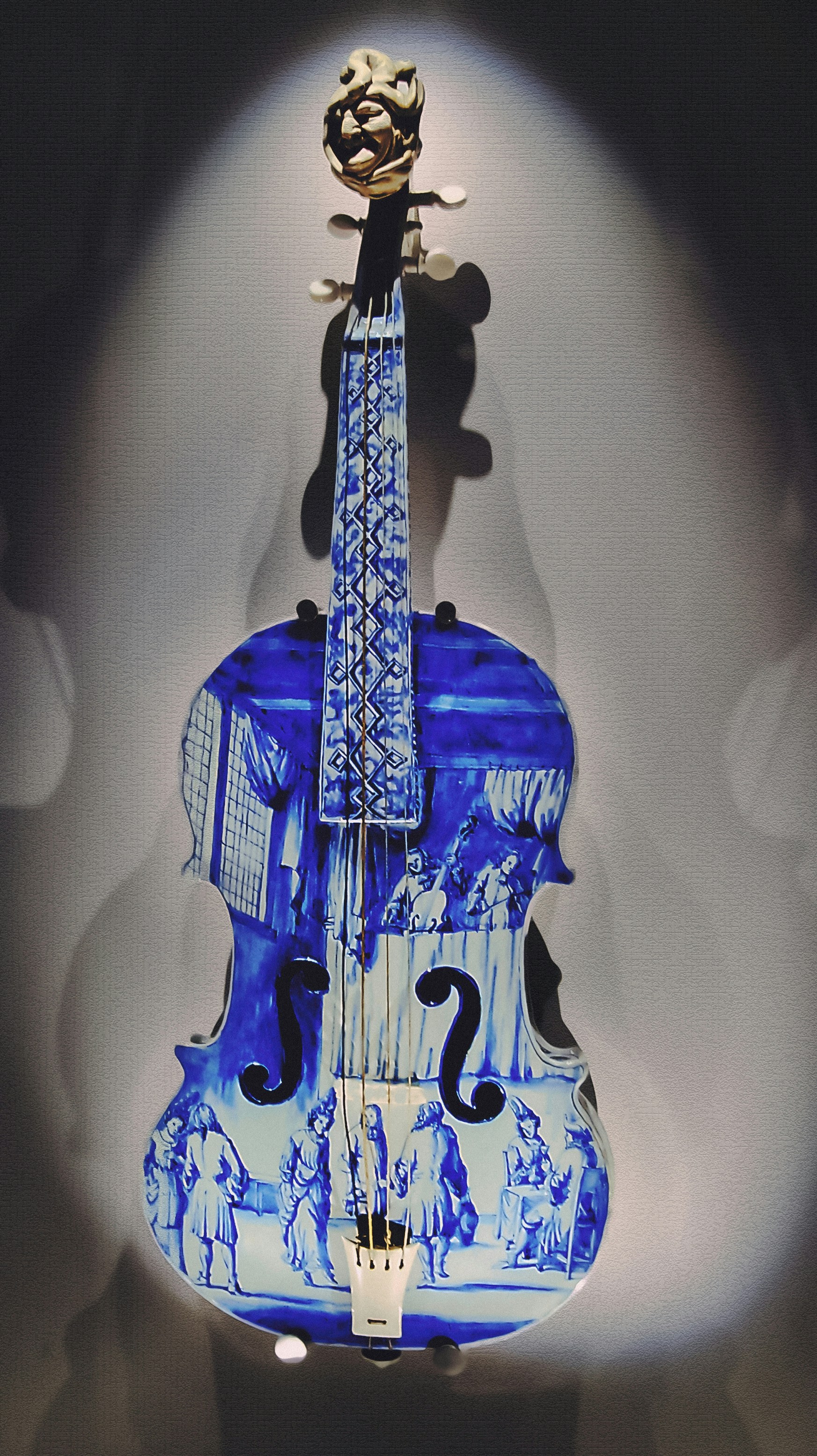 Intricately designed ceramic violin adorned with blue and white illustrations, showcasing a theatrical scene. The artwork highlights the fusion of music and visual art.