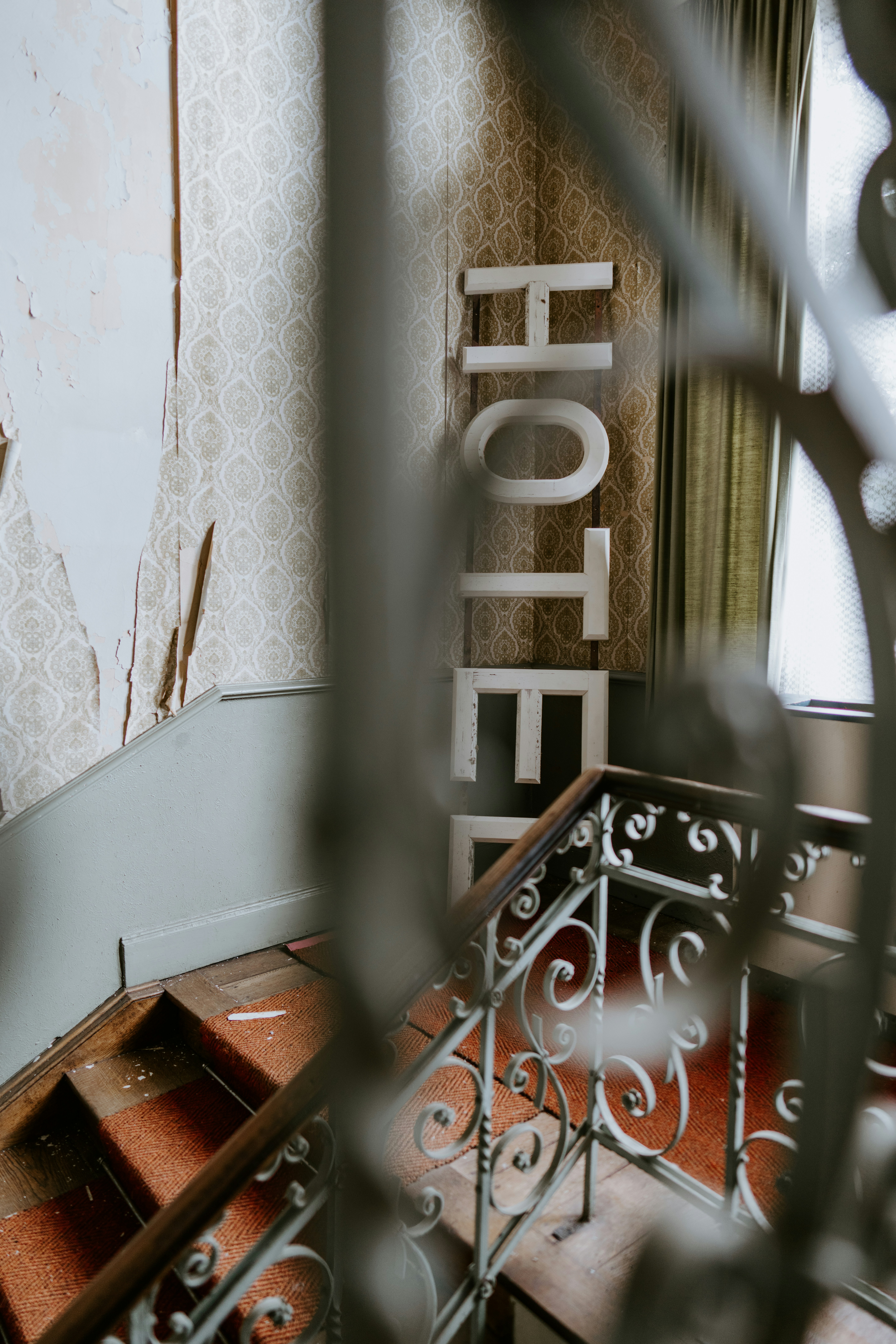 Vertical HOTEL Sign Against a Peeling Stairwell with Ornate Ironwork