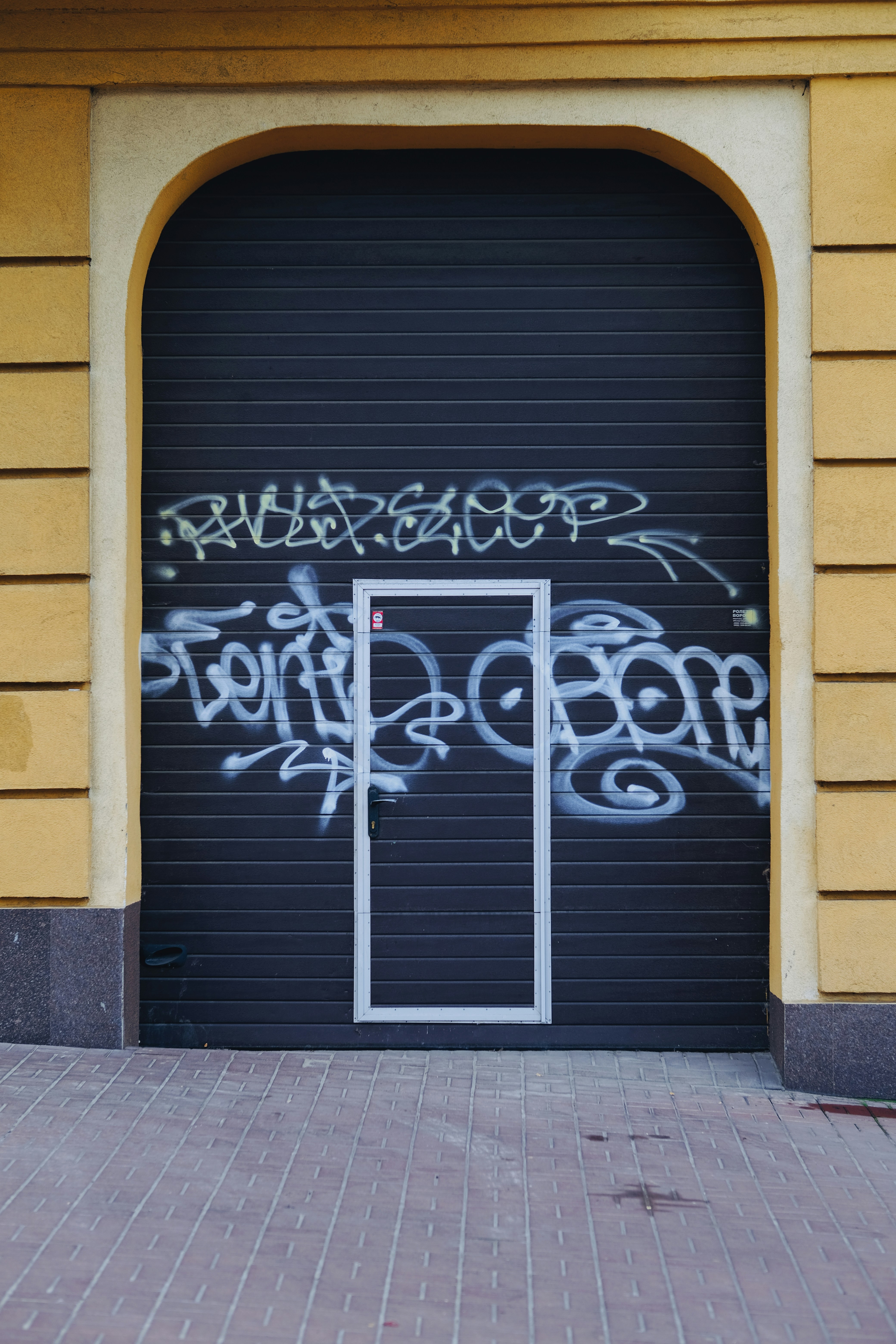 Hidden Gate Behind Graffiti in a Sunlit Yellow Archway