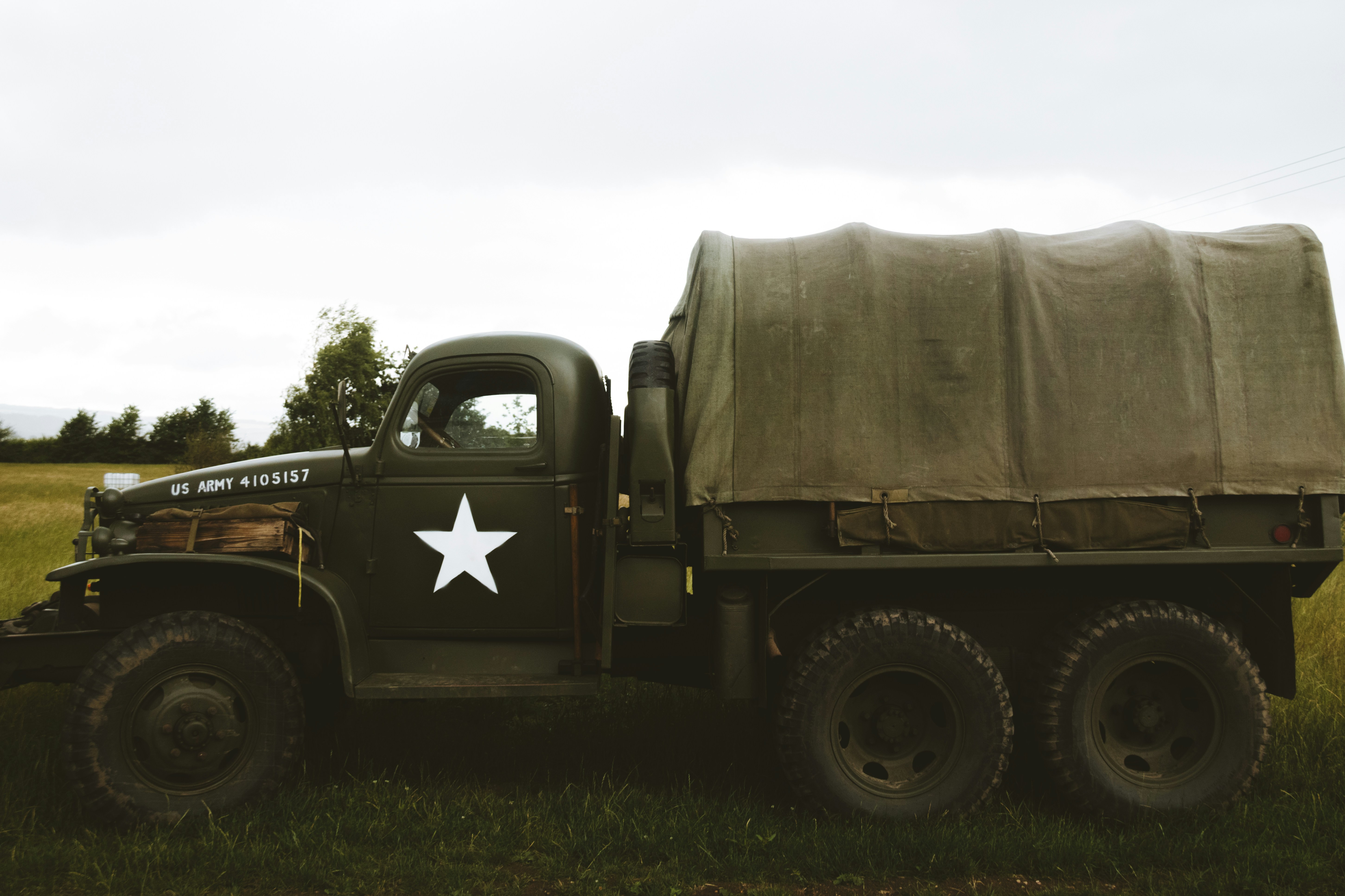 Classic military truck adorned with a star insignia, parked in a grassy field under a cloudy sky.