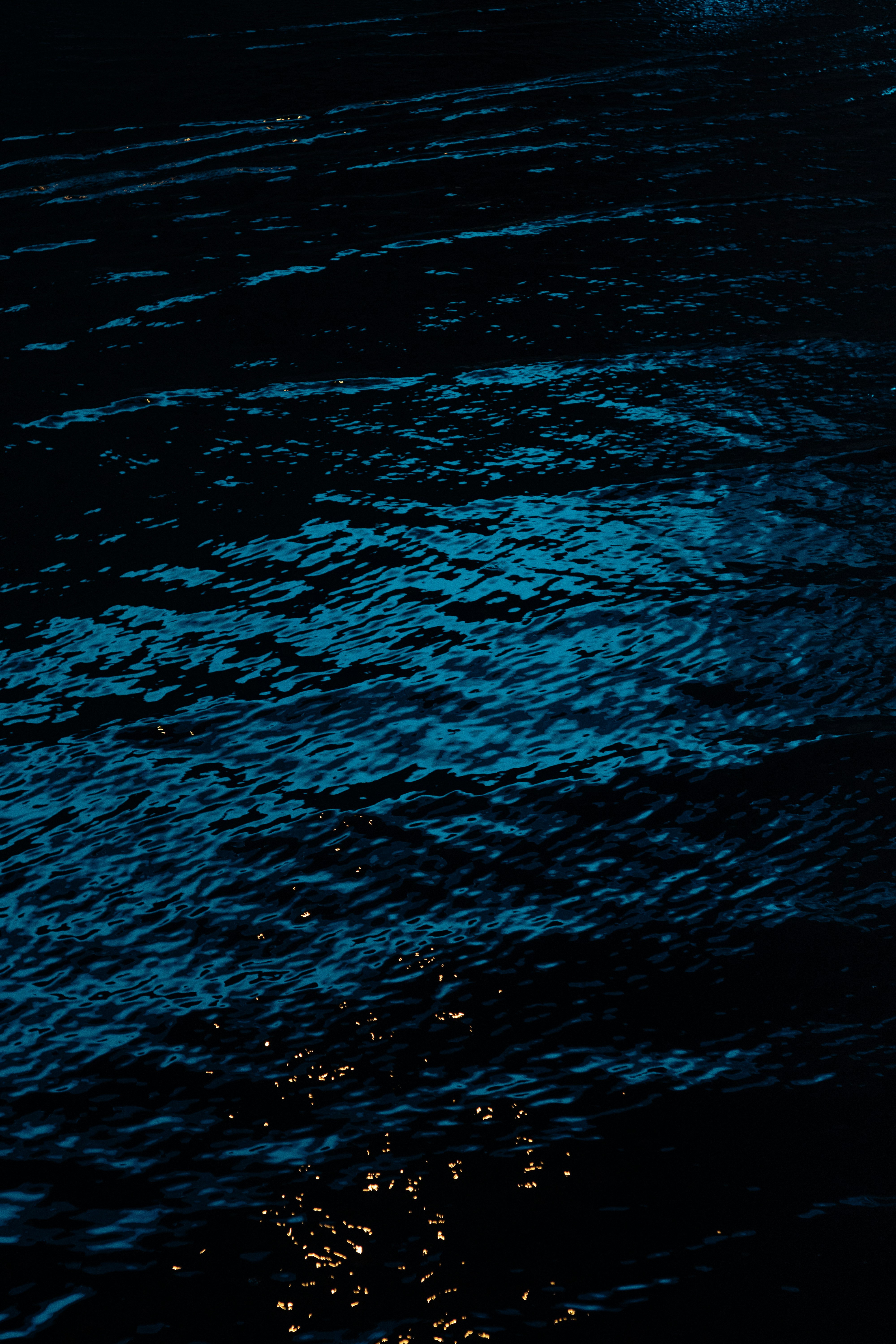 Rippling dark waters illuminated by soft glimmers, creating a serene atmosphere. The interplay of light and shadow evokes a tranquil evening by the water.