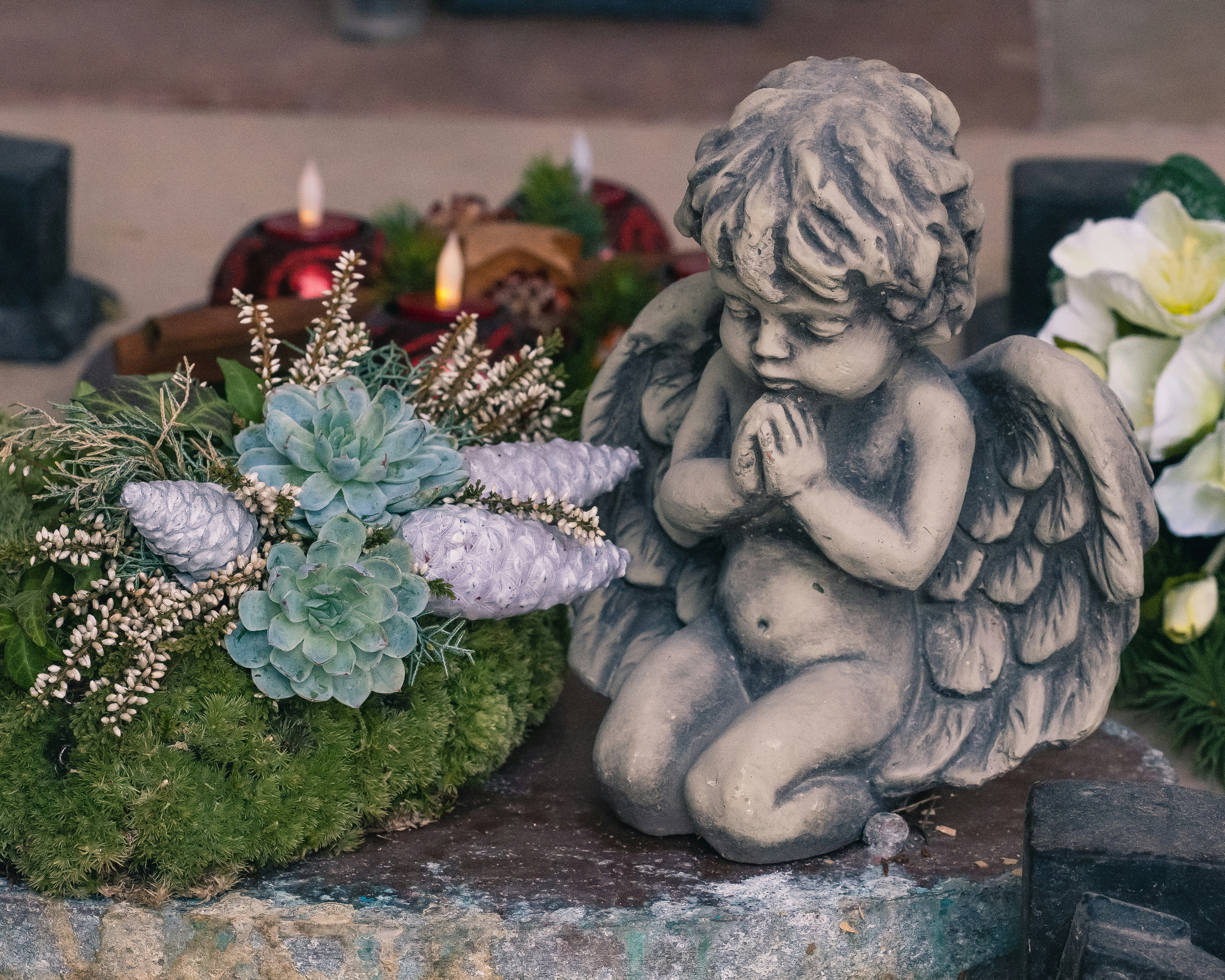 Stone cherub statue beside floral arrangement and lit candles.