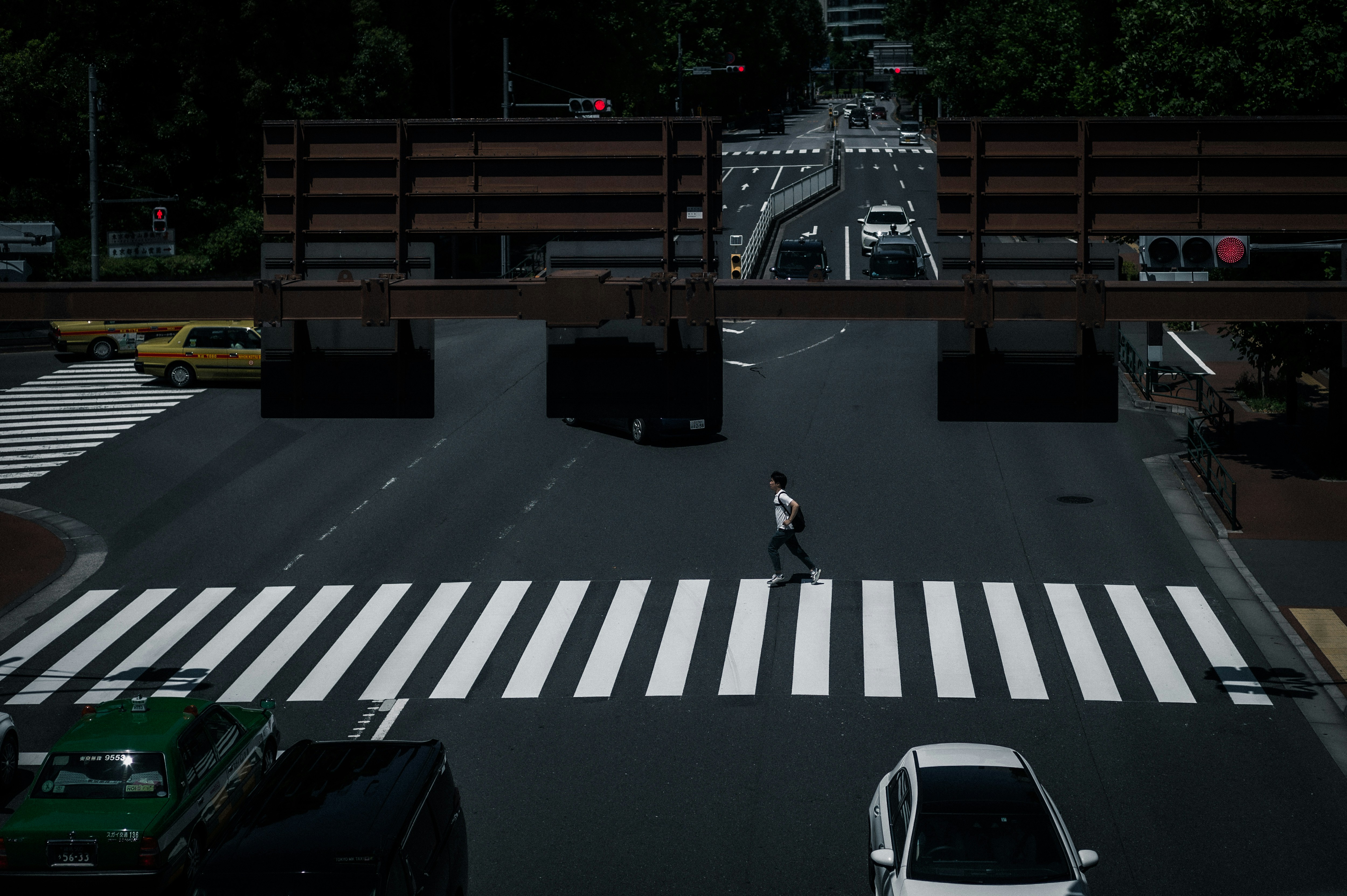 A lone pedestrian crosses a busy intersection, surrounded by vehicles and stark white crosswalks. The scene captures the essence of city life.