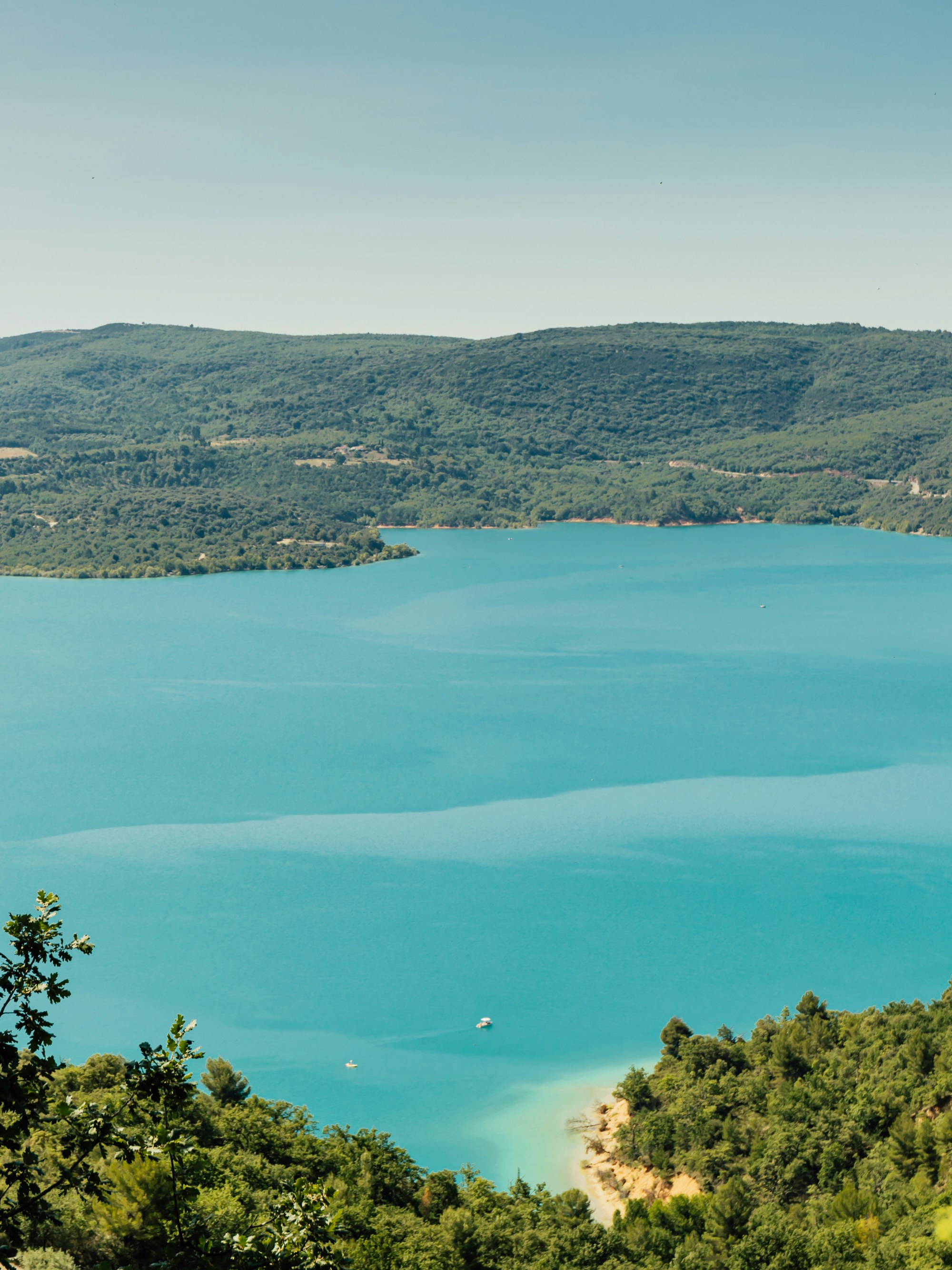 Vibrant turquoise lake surrounded by lush greenery and rolling hills under a clear sky.