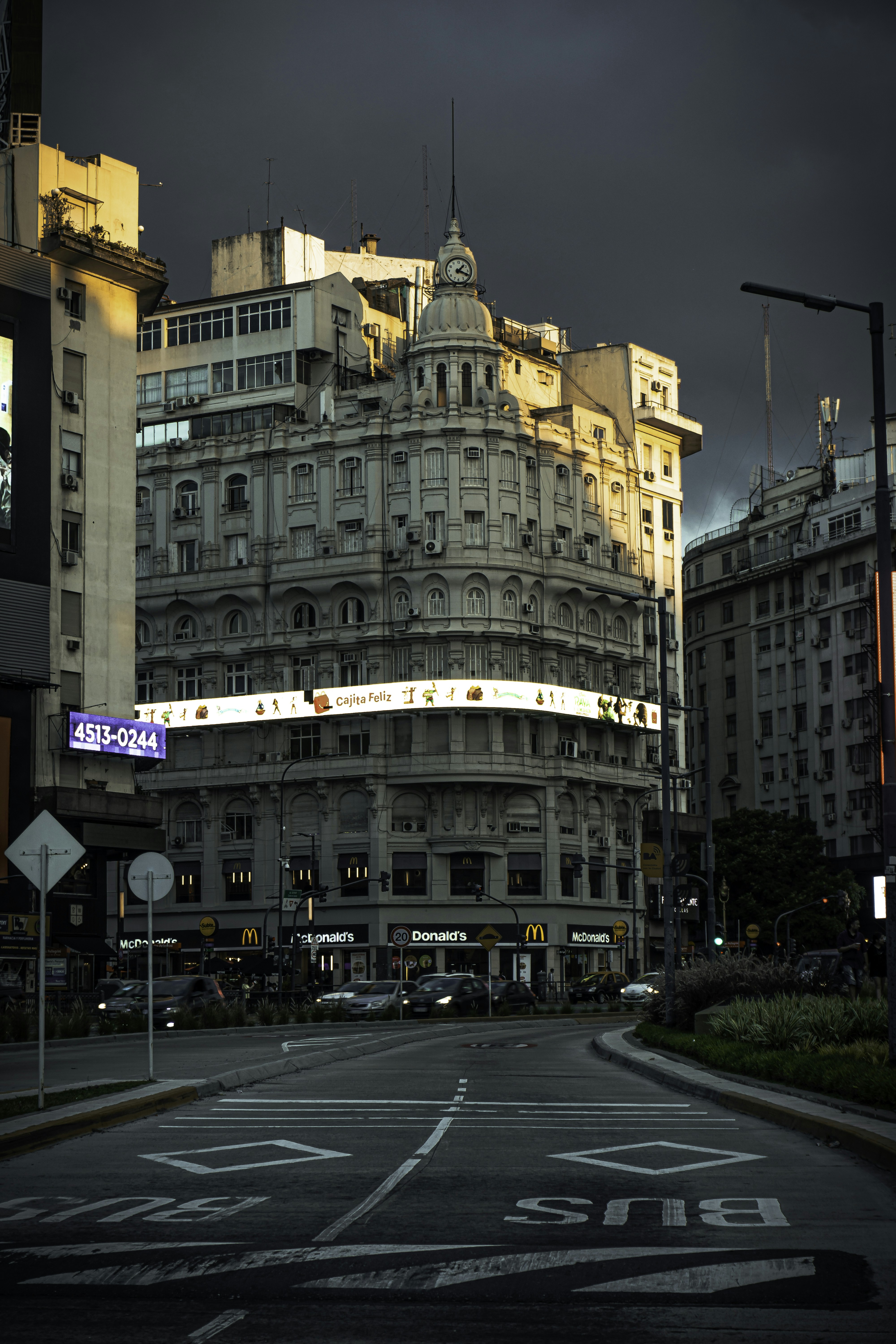 Historic building with intricate architecture illuminated by streetlights, set against a dark, moody sky. Neon signs and urban elements add a contemporary touch.