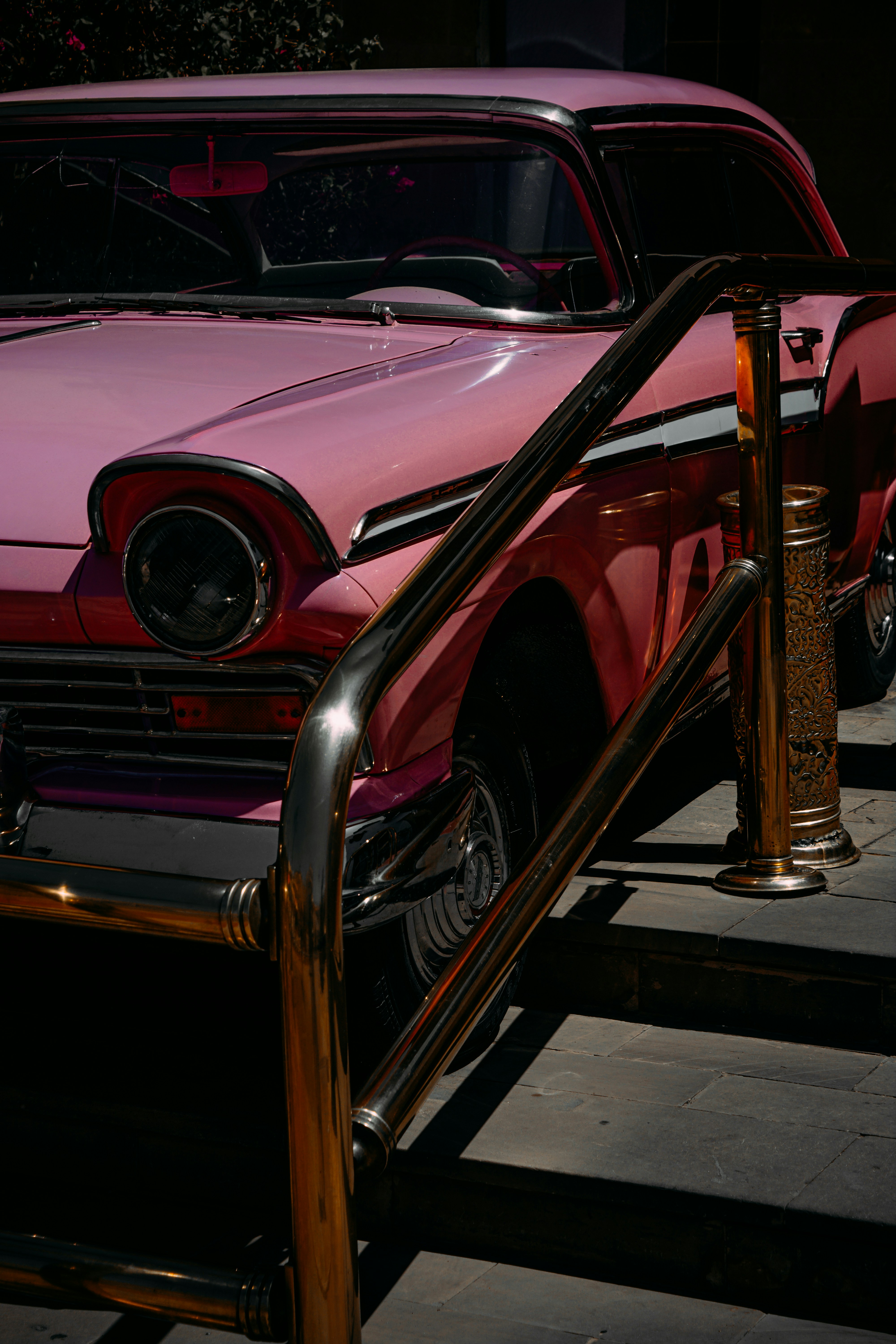 A vintage pink car partially obscured by a golden railing, showcasing its elegant curves and classic design.