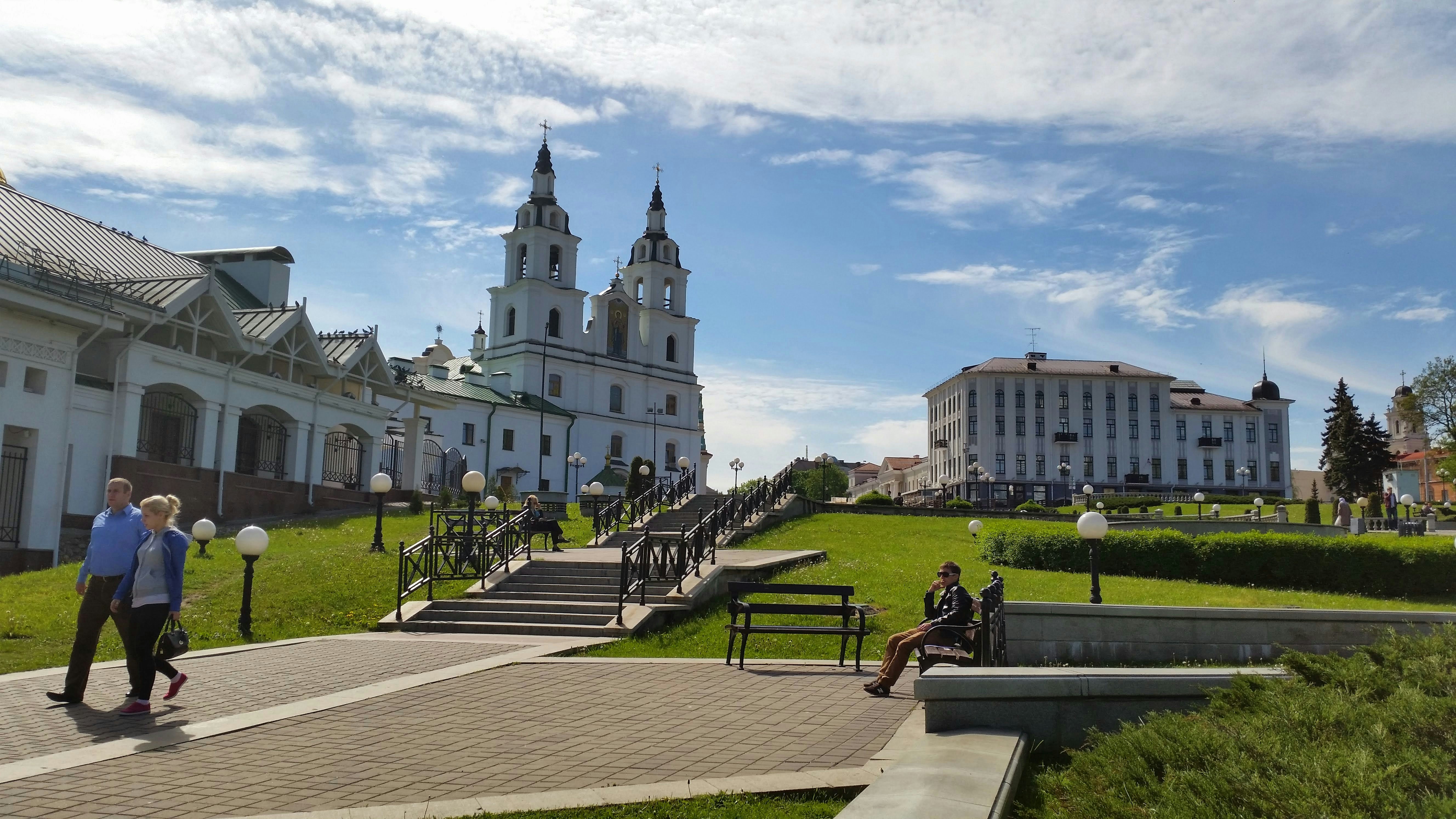 People walking near a historic church with twin spires under a partly cloudy sky.