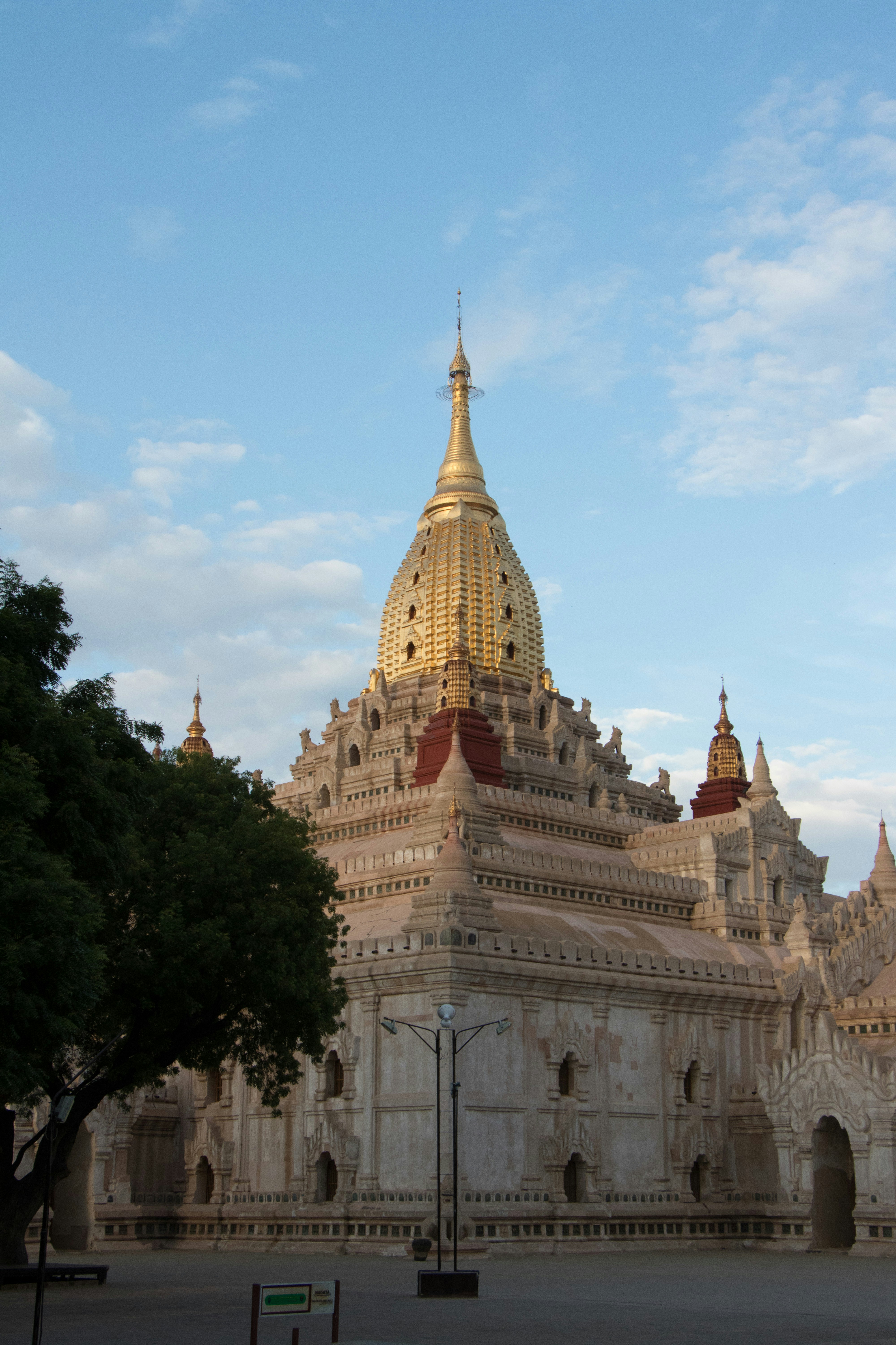 Intricate temple architecture with a gleaming golden spire under a blue sky, surrounded by lush greenery.