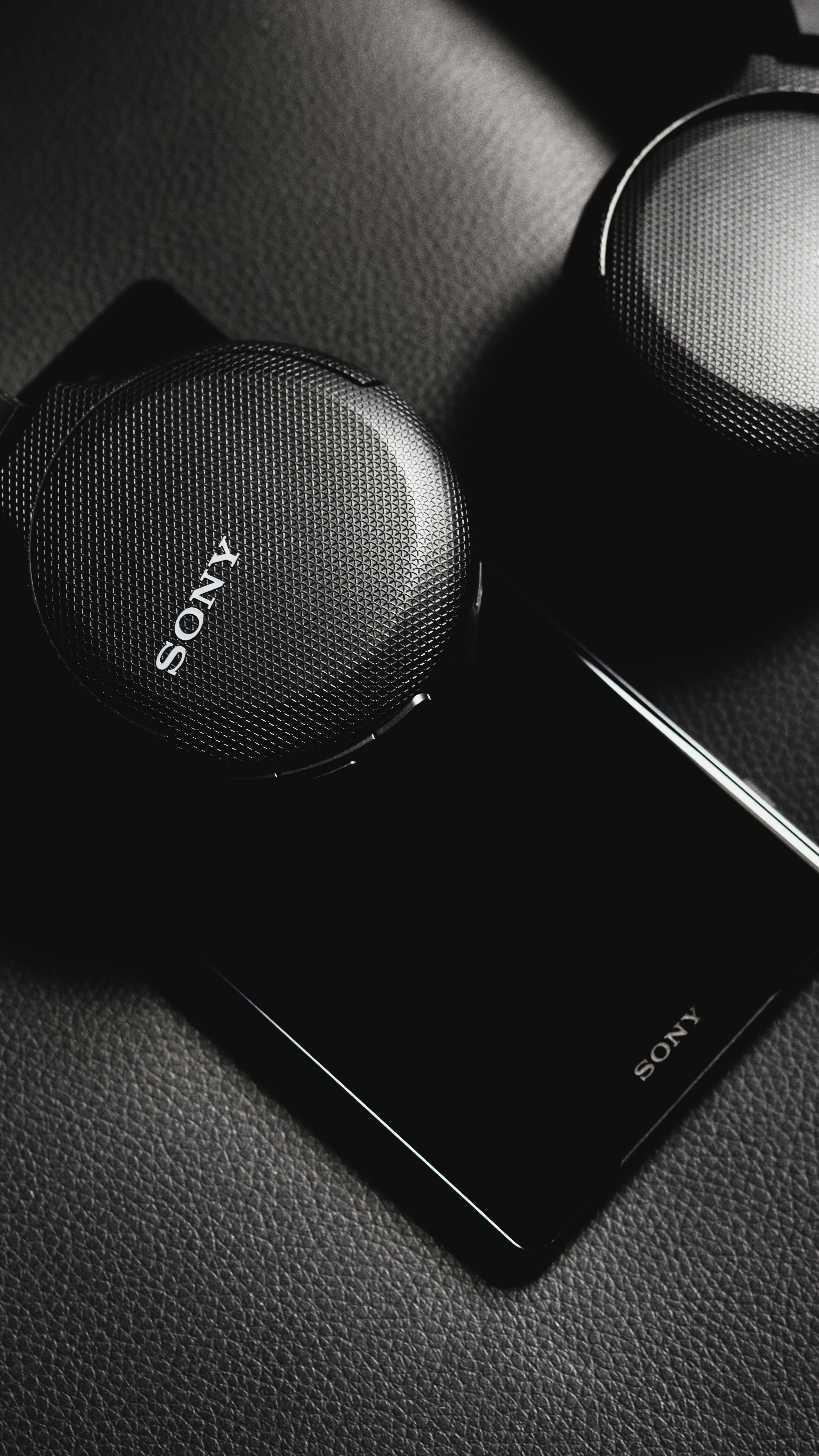 Black Sony headphones resting on a sleek smartphone, showcasing a minimalist aesthetic on a textured surface.