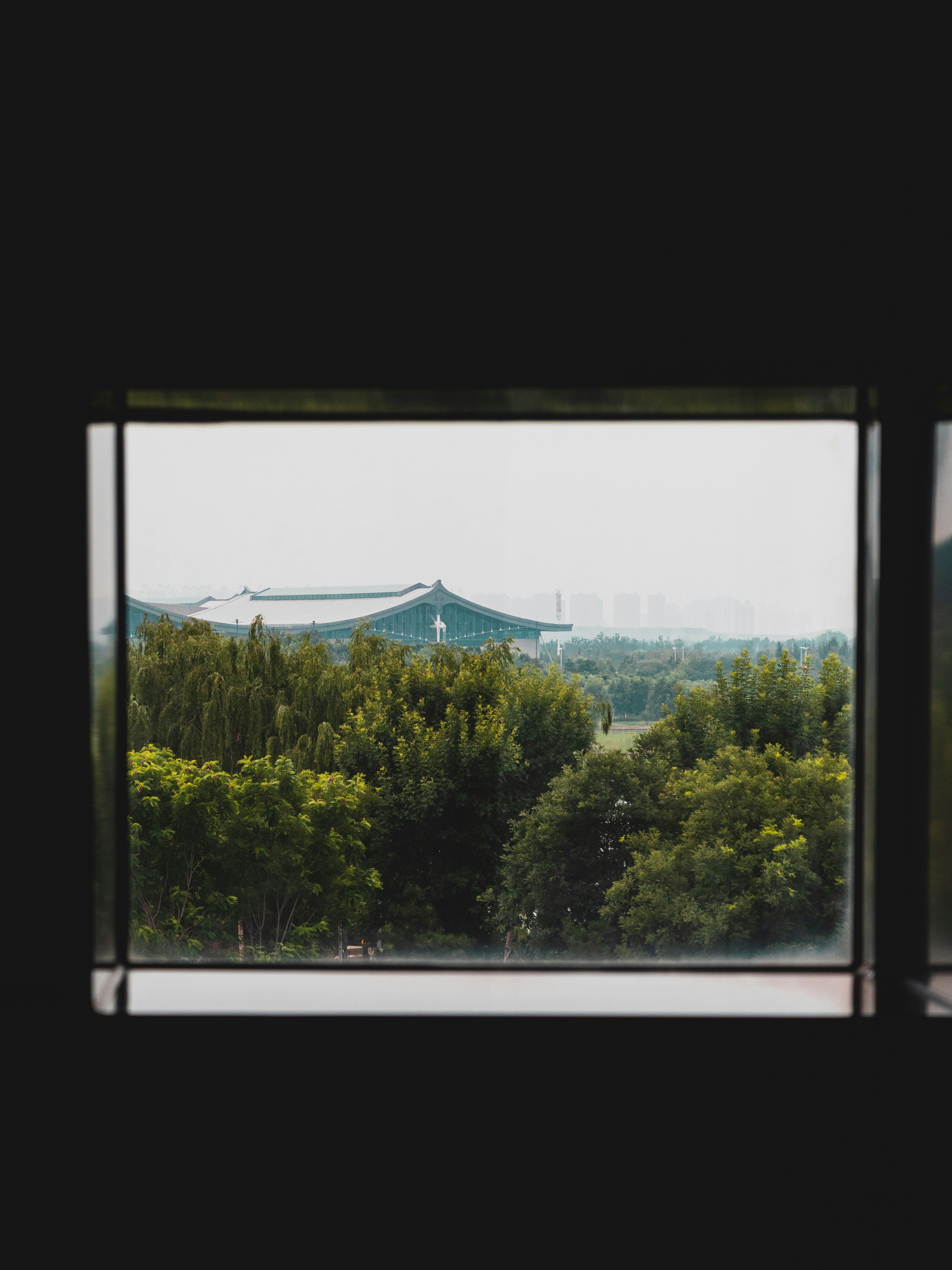 A lush green landscape framed by a window, showcasing a modern architectural structure in the background. The scene captures a tranquil blend of nature and design.